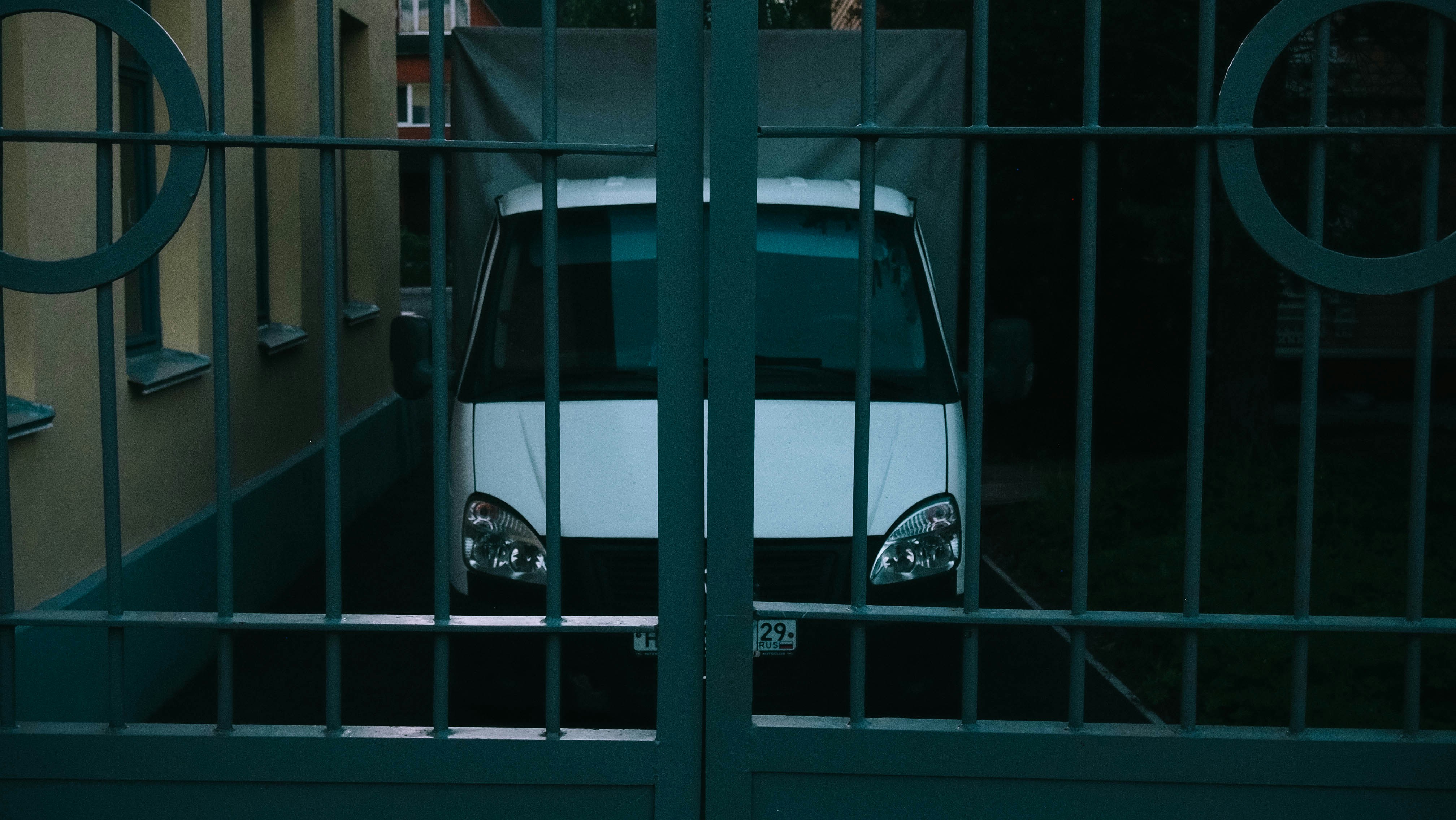 White van parked directly behind a metal gate in a dimly lit alleyway.