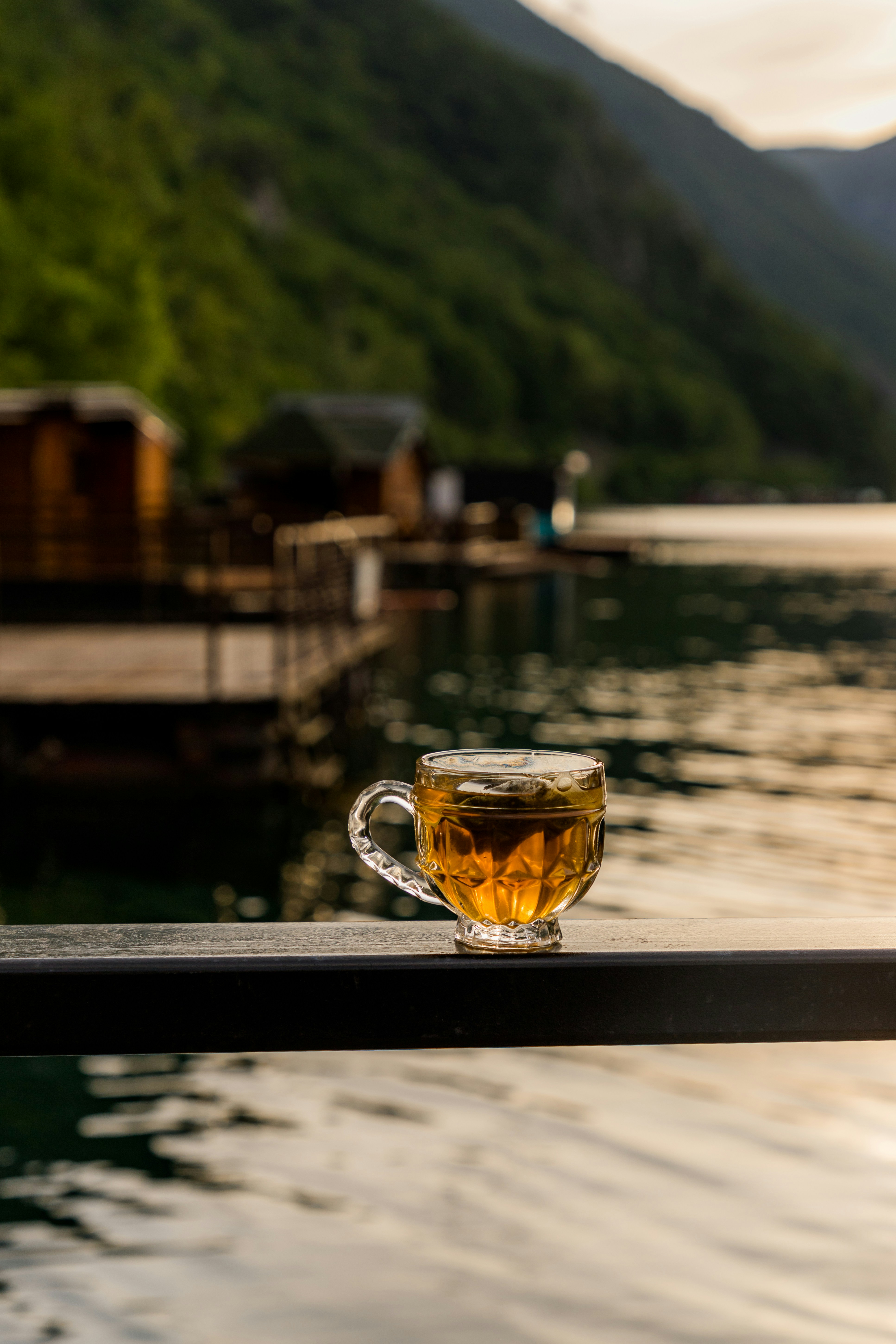A glass of tea overlooking a sunset on a lake | A cup of tea sitting on top of a table next to a body of water
