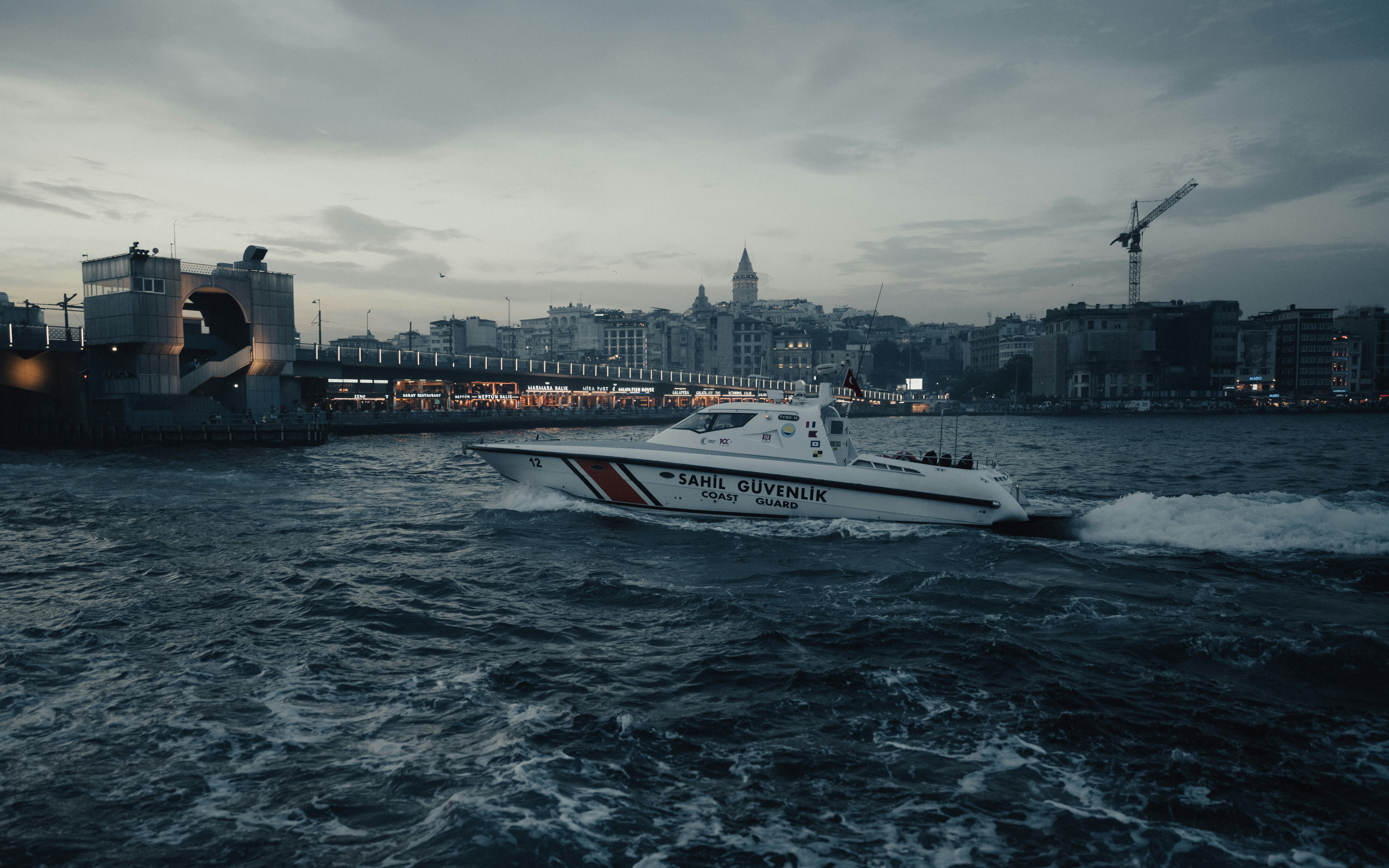 Dusk Wake: White Speedboat Carves Through Choppy Harbor Beneath a Distant Cityscape