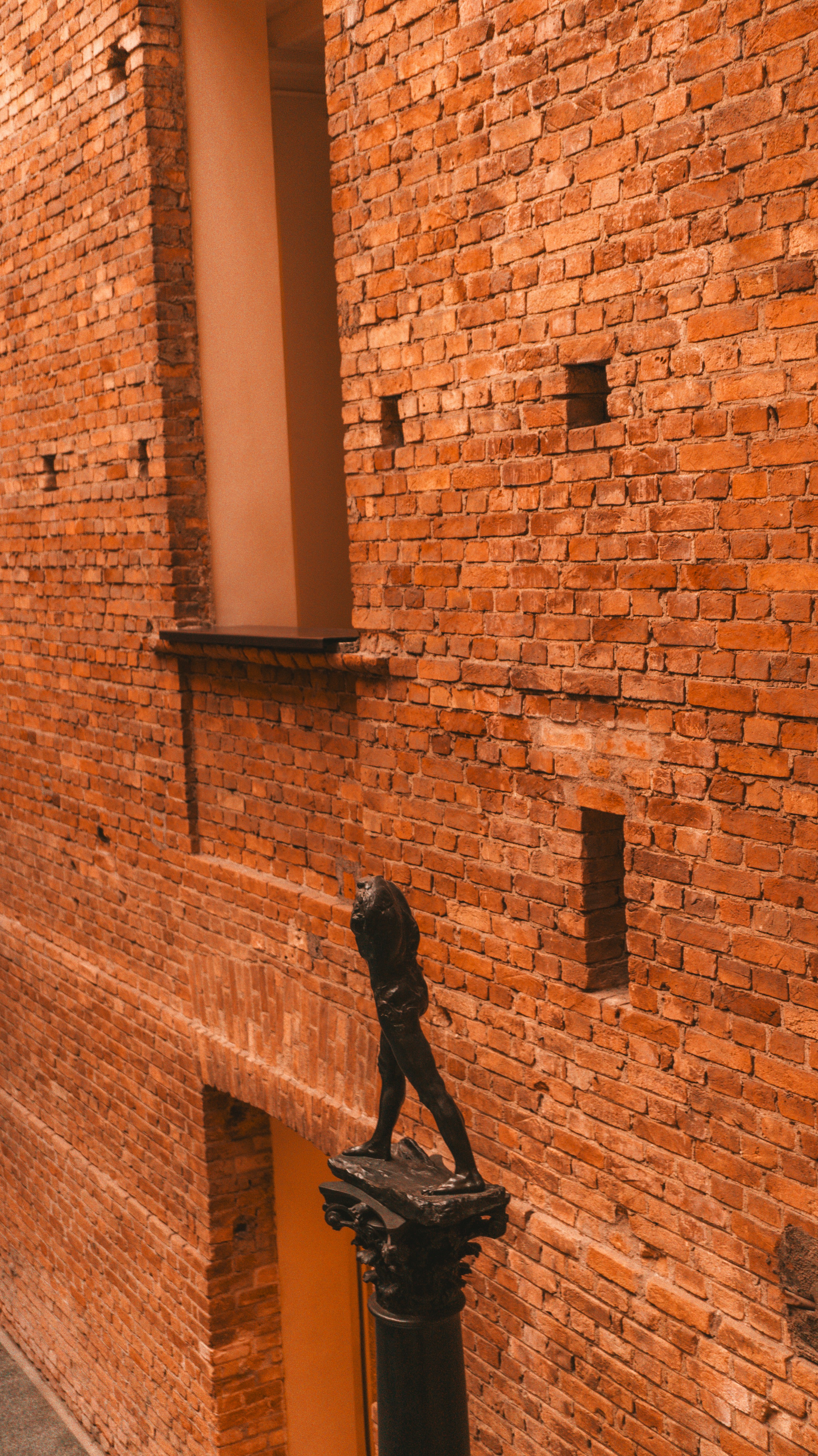 Brickbound Sentinel: Lone Figure on a Column Against Warm Brickwork