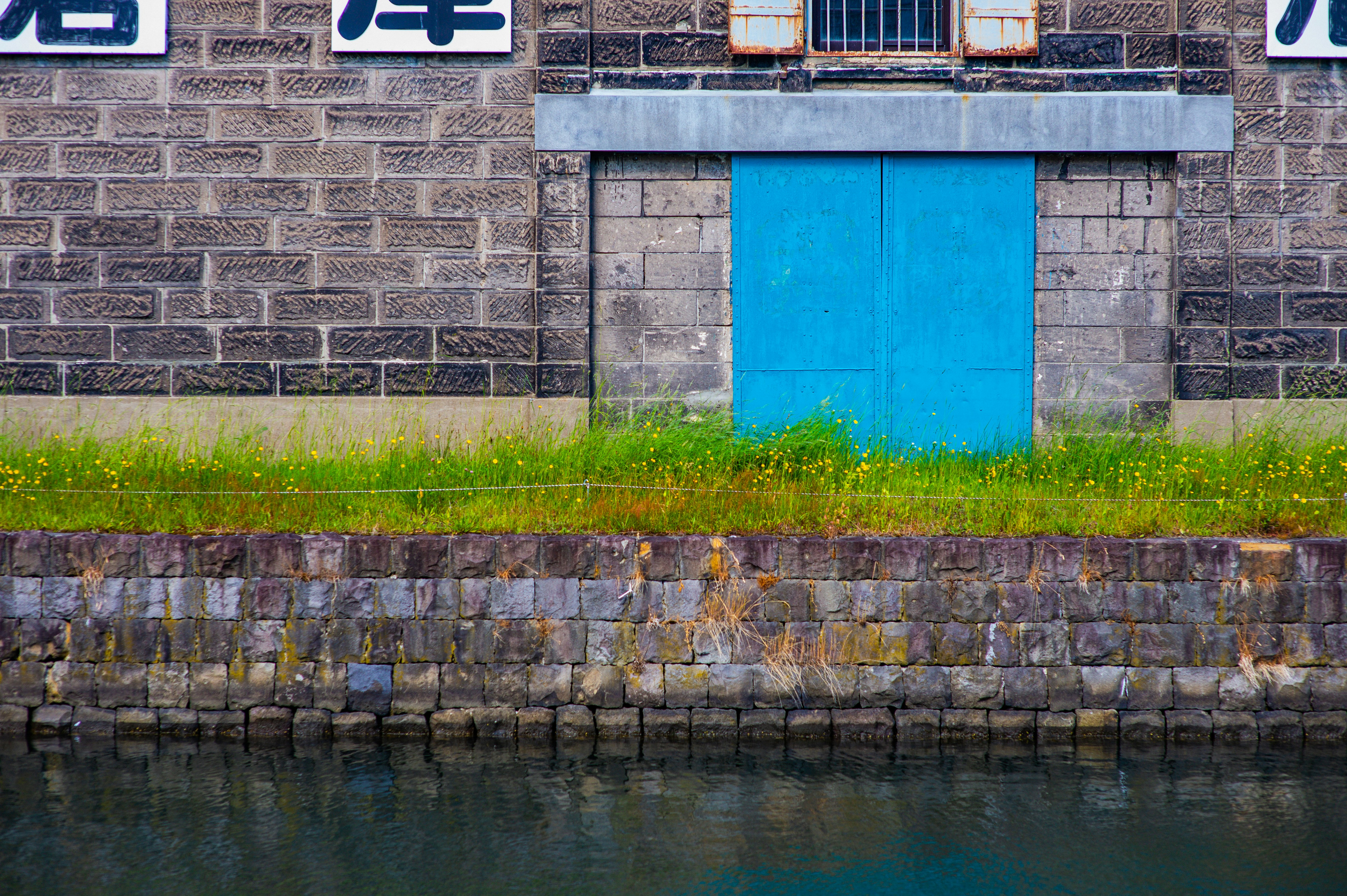Azure Gate by the River: a solitary blue door in a weathered brick facade