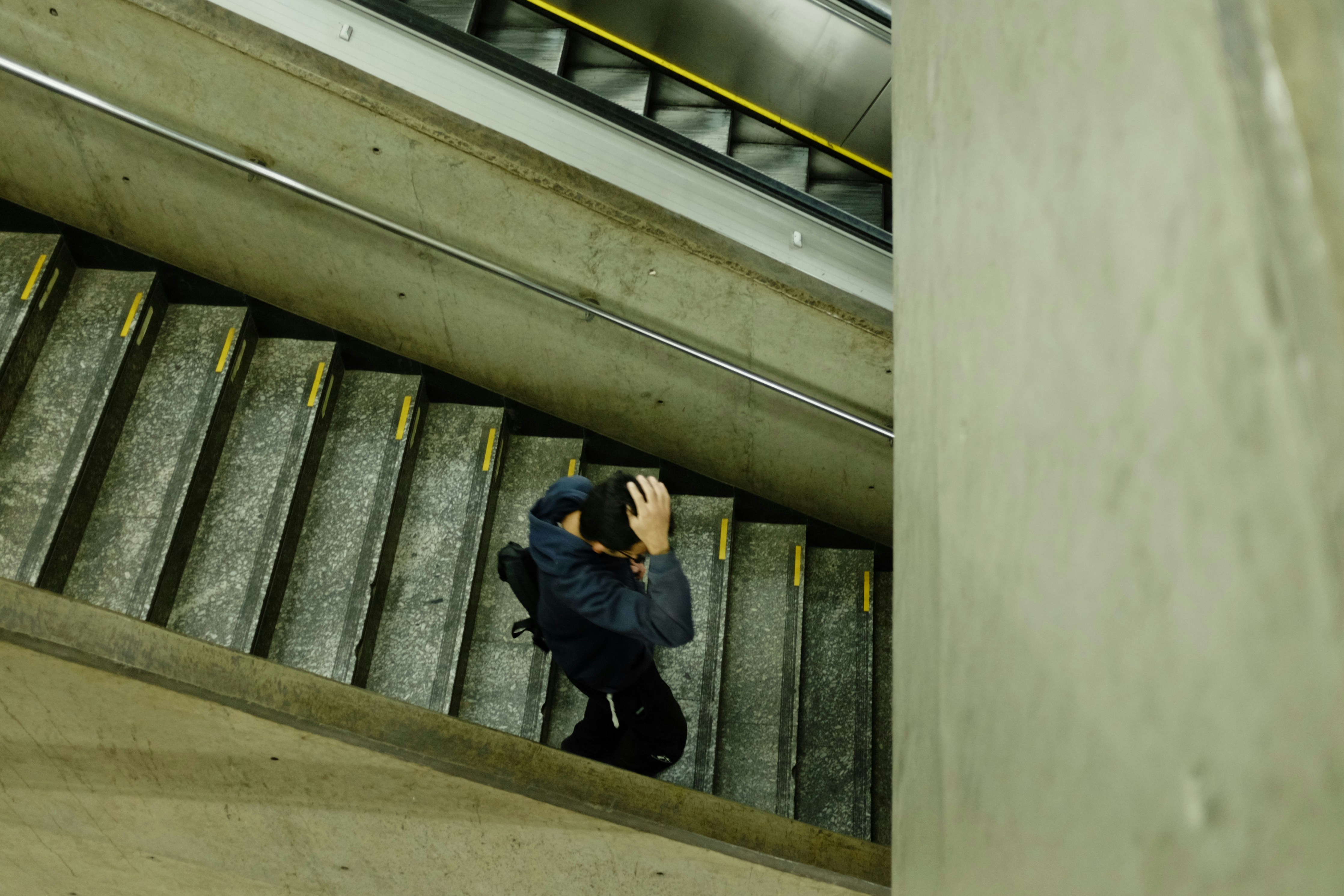 Person ascending a dimly lit escalator with concrete surroundings.