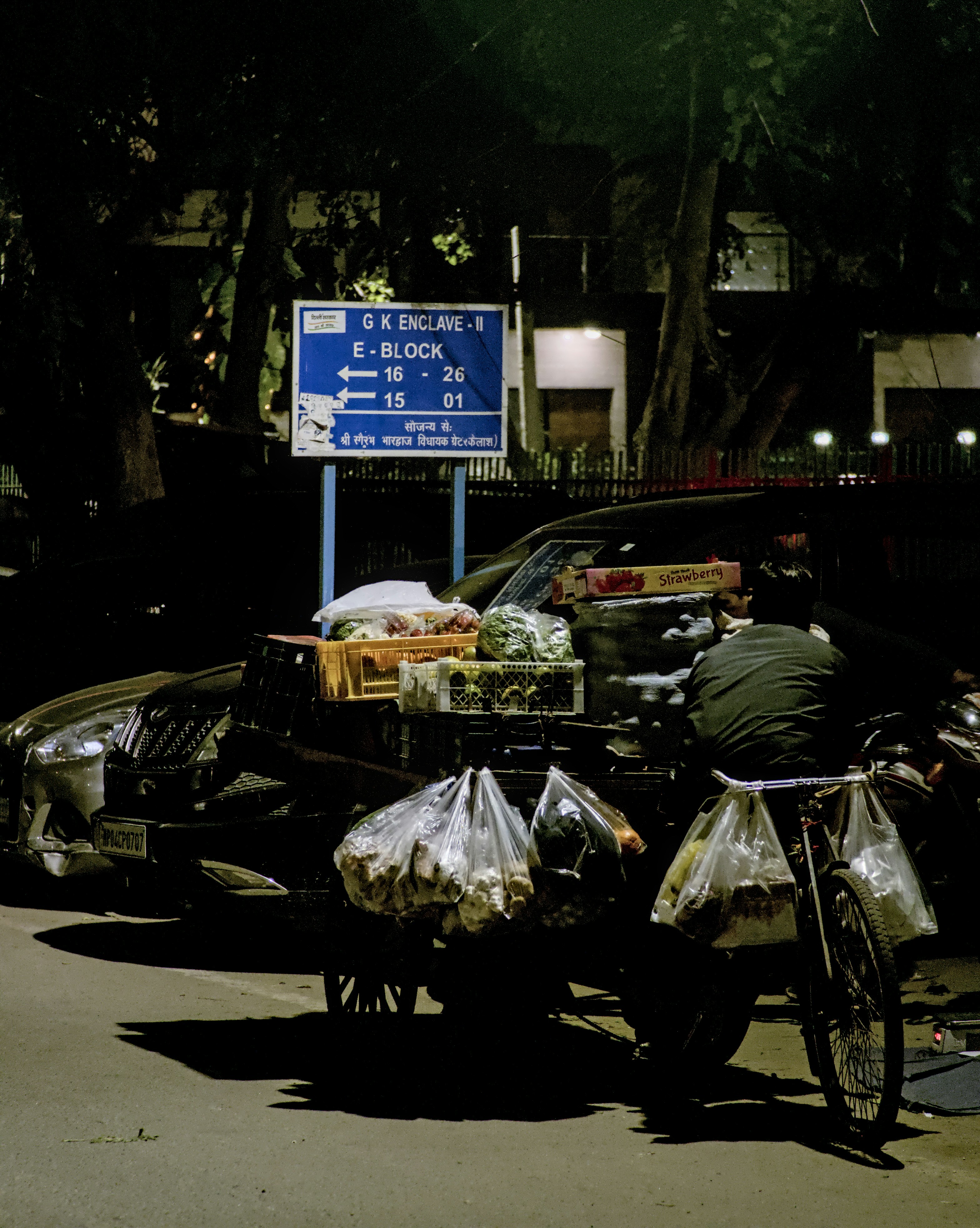 A Vegetable vendor looking for customers outside my house | A man riding a bike down a street next to a car
