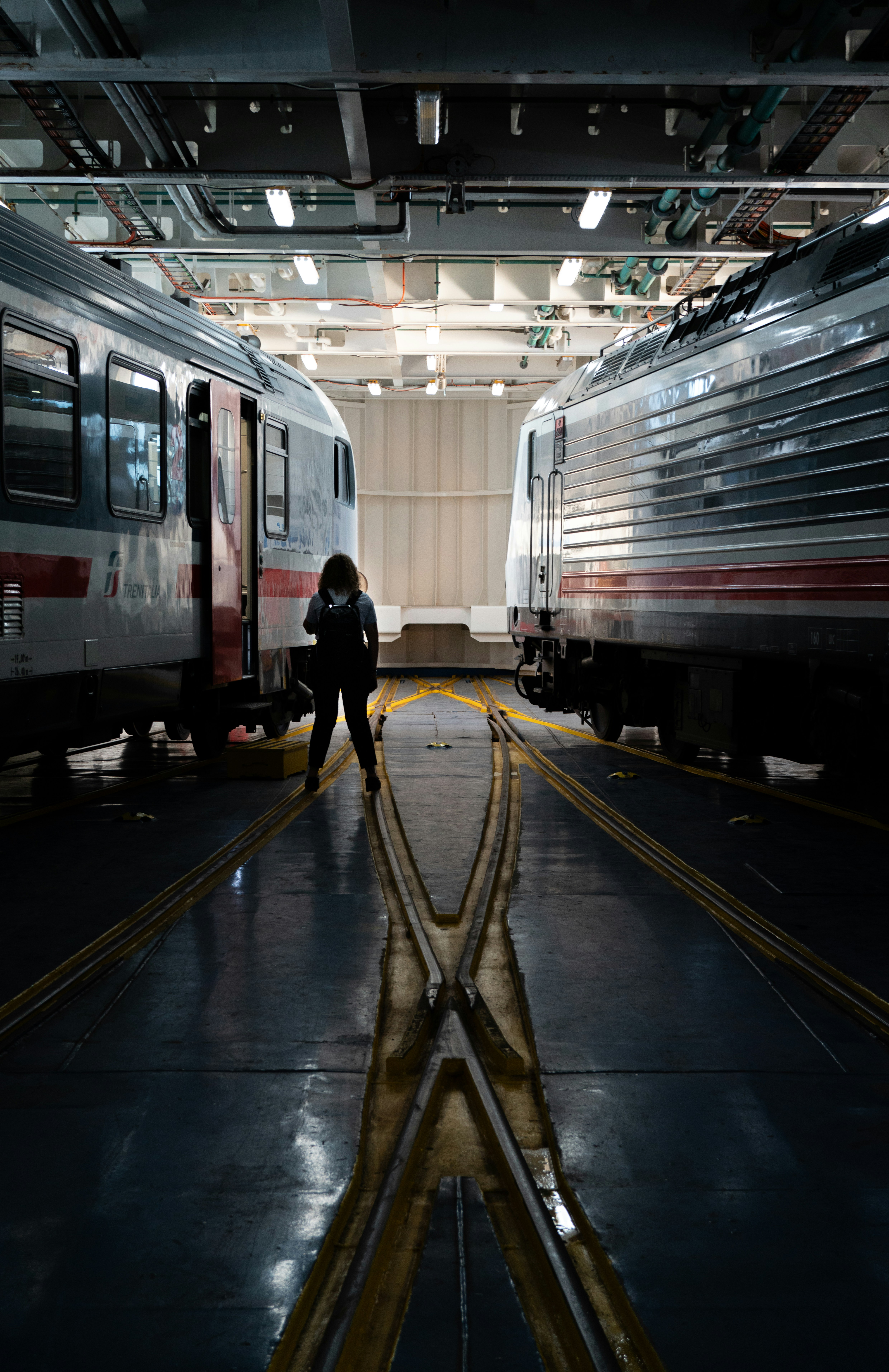 Between Iron Giants: A lone figure framed by rails in a dim maintenance bay
