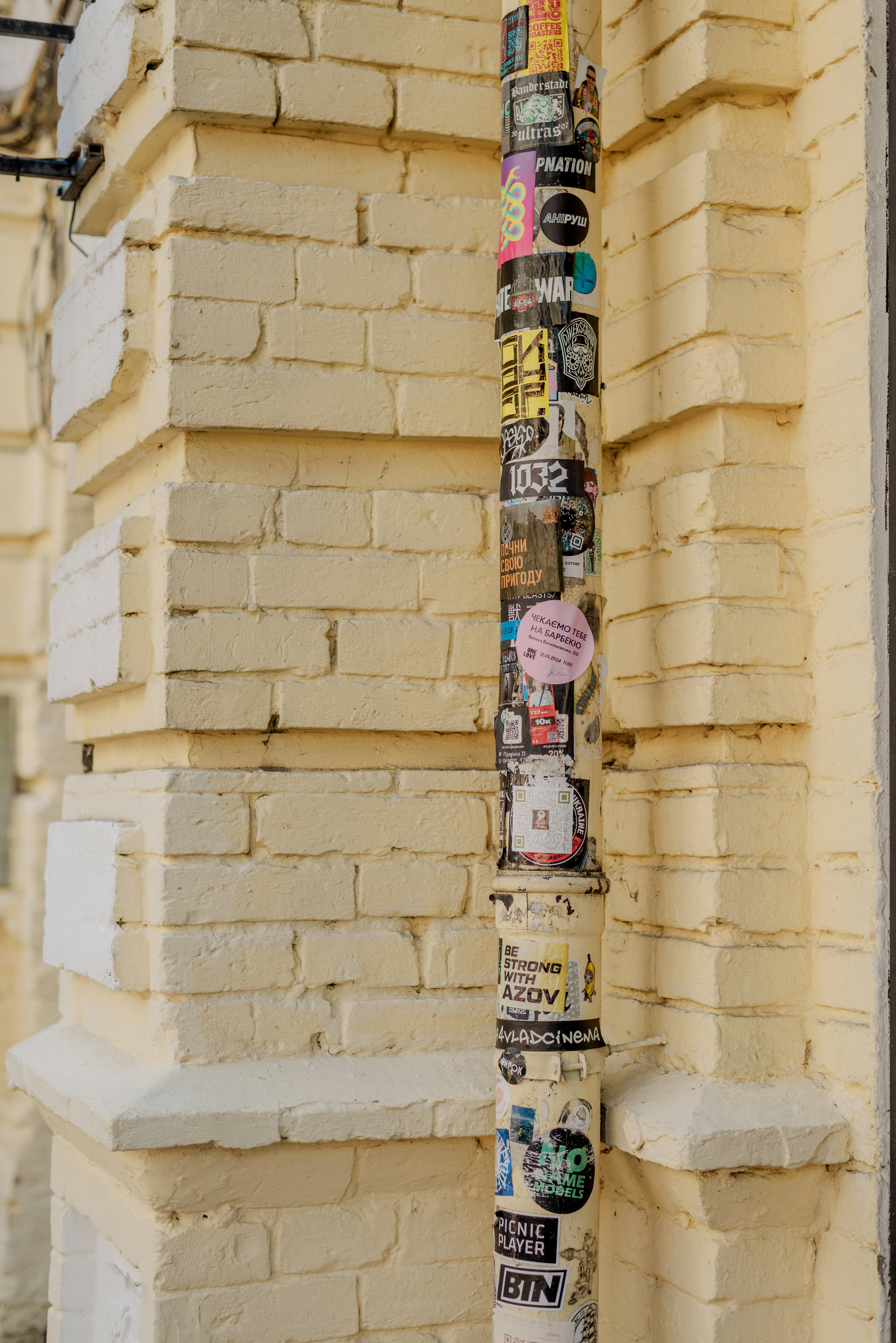 Stickered Pillar: A Sunlit Urban Mosaic on Yellow Brick