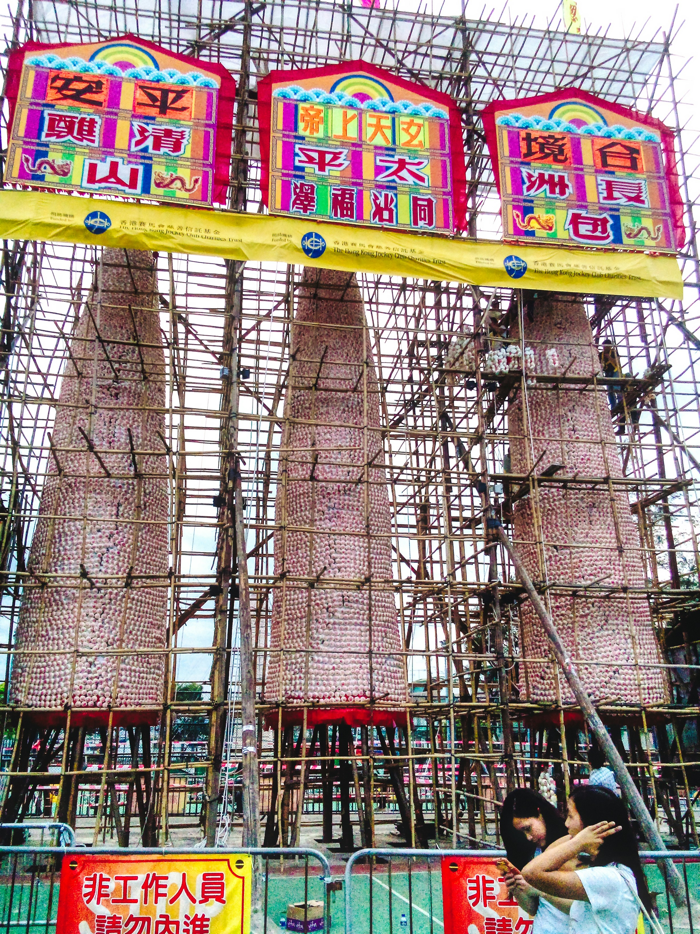 Crimson Banners Crown a Bamboo Scaffold: A Street-Side Construction Scene in Full Color