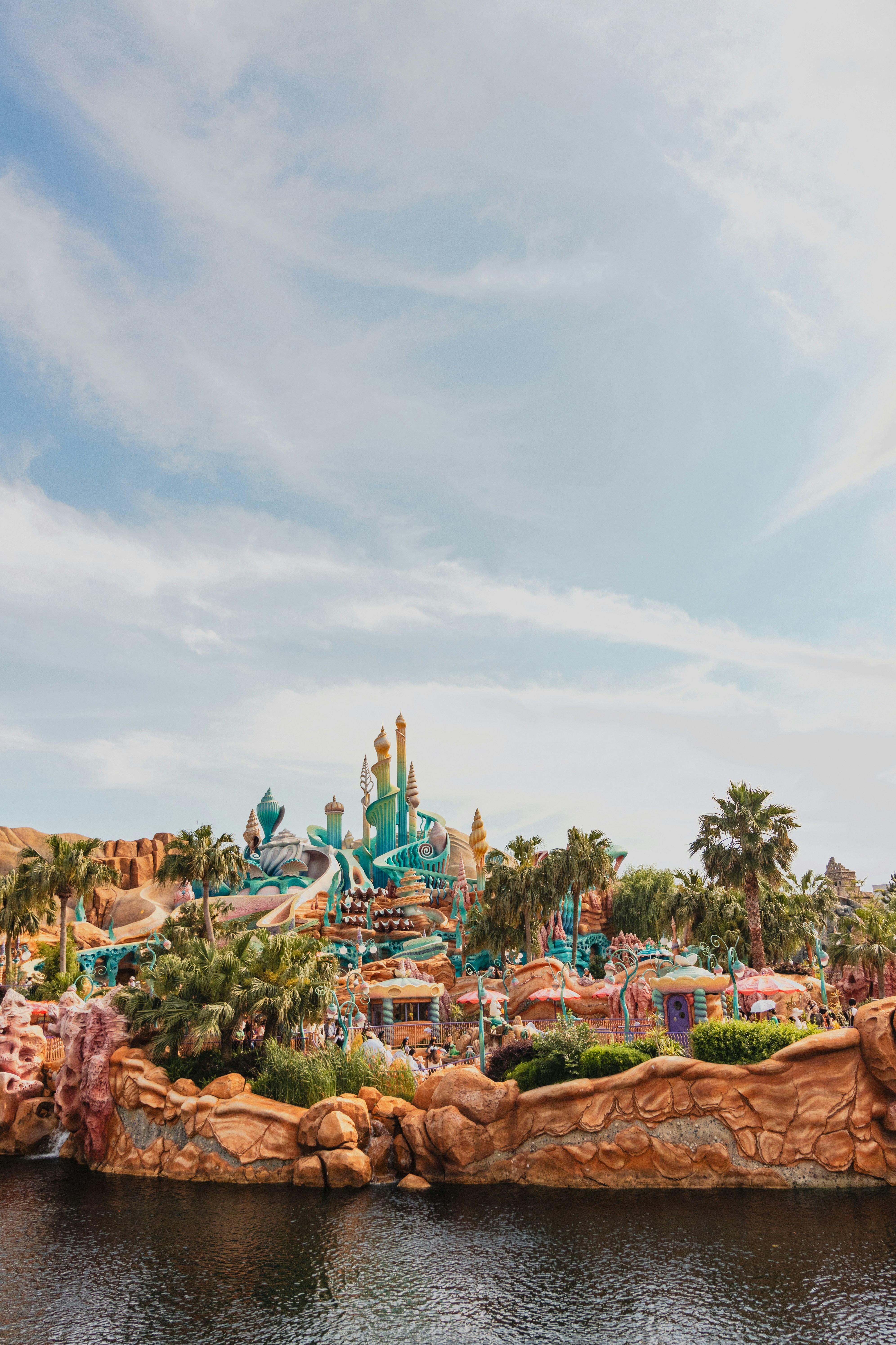 Vibrant theme park landscape featuring colorful architecture and lush palm trees by a tranquil water body.