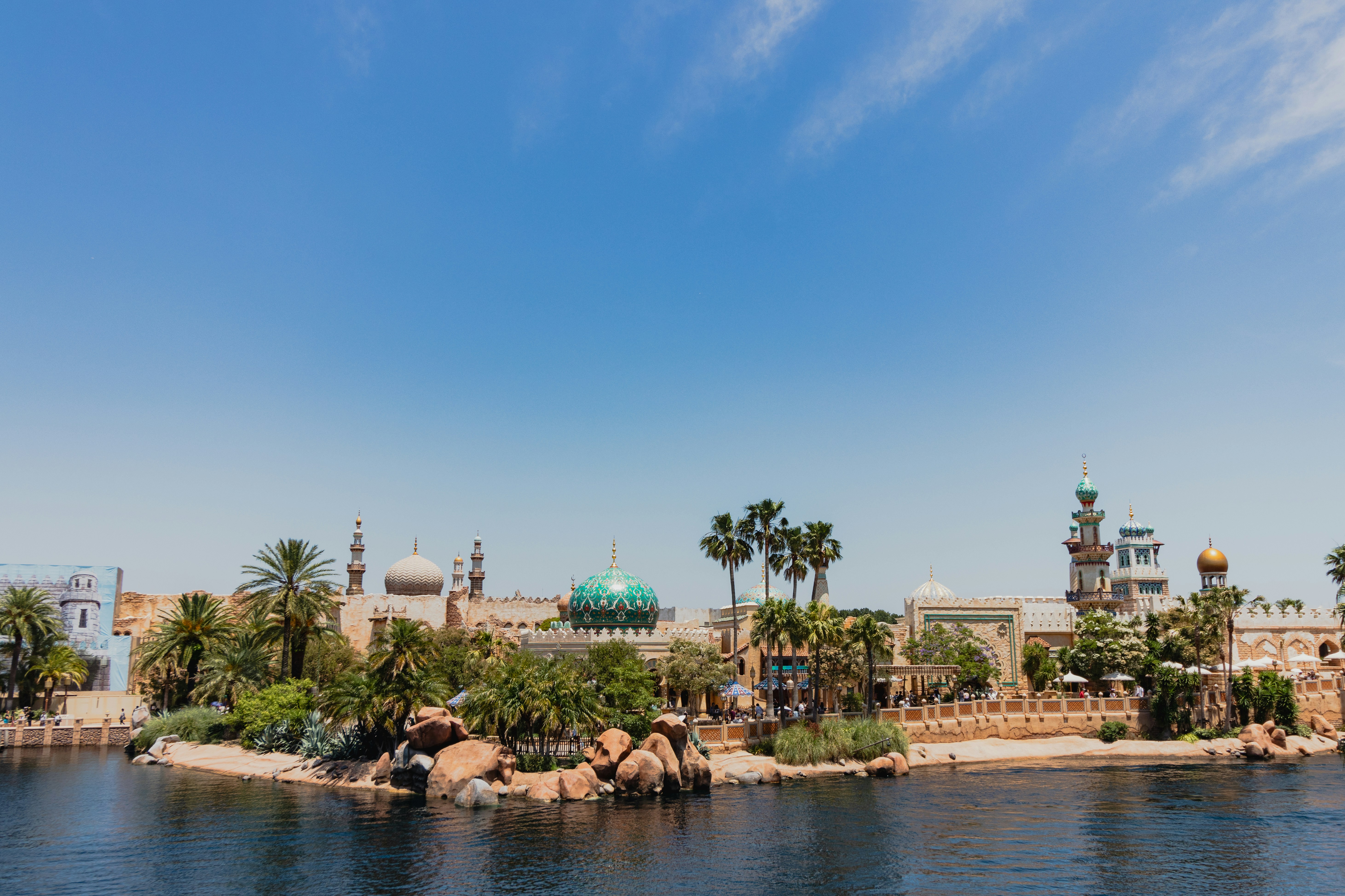 Palm trees and structures line a serene waterfront under a clear blue sky.