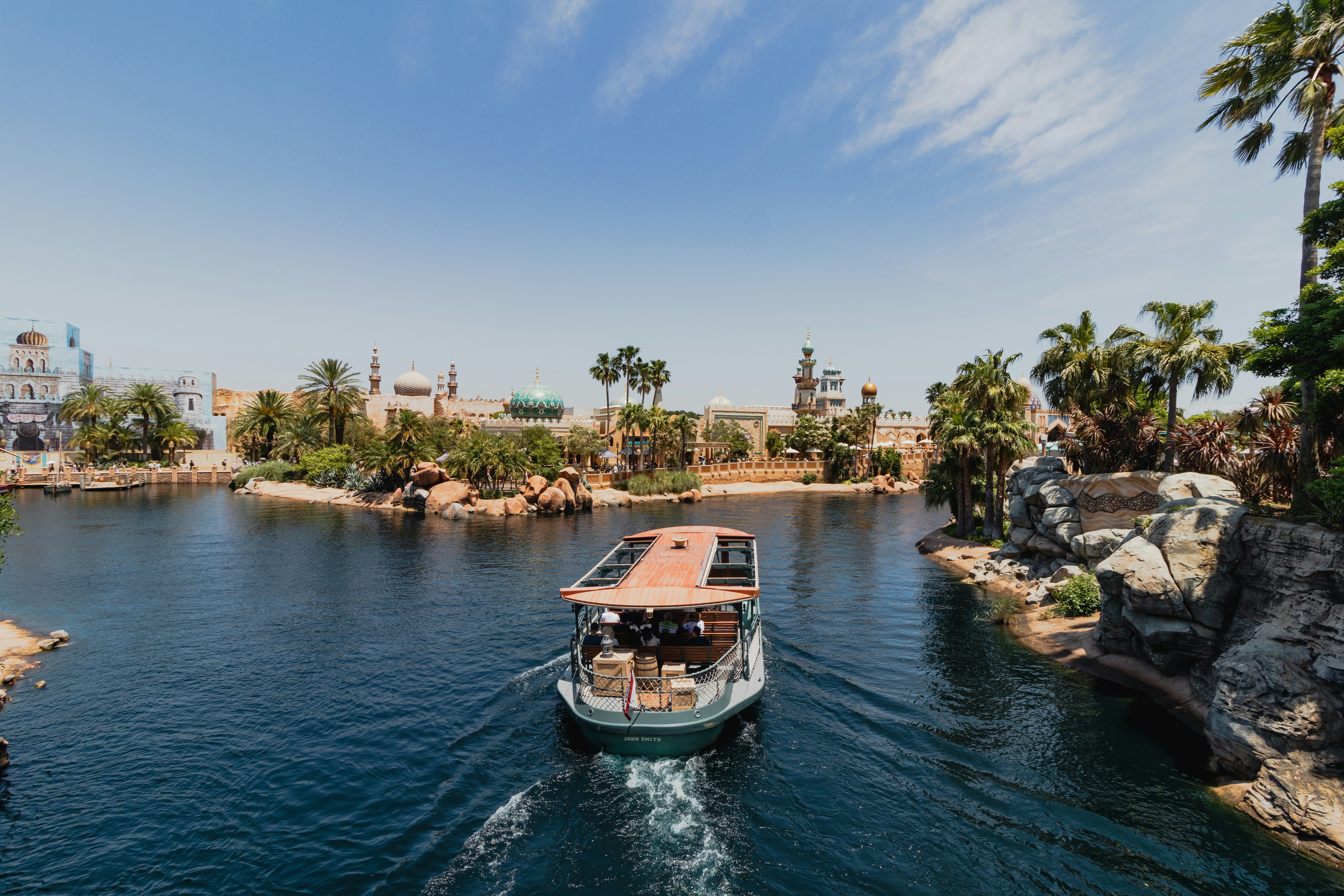 Palm-Shaded Canal Passage: A Sunlit Boat Through a Themed Waterfront