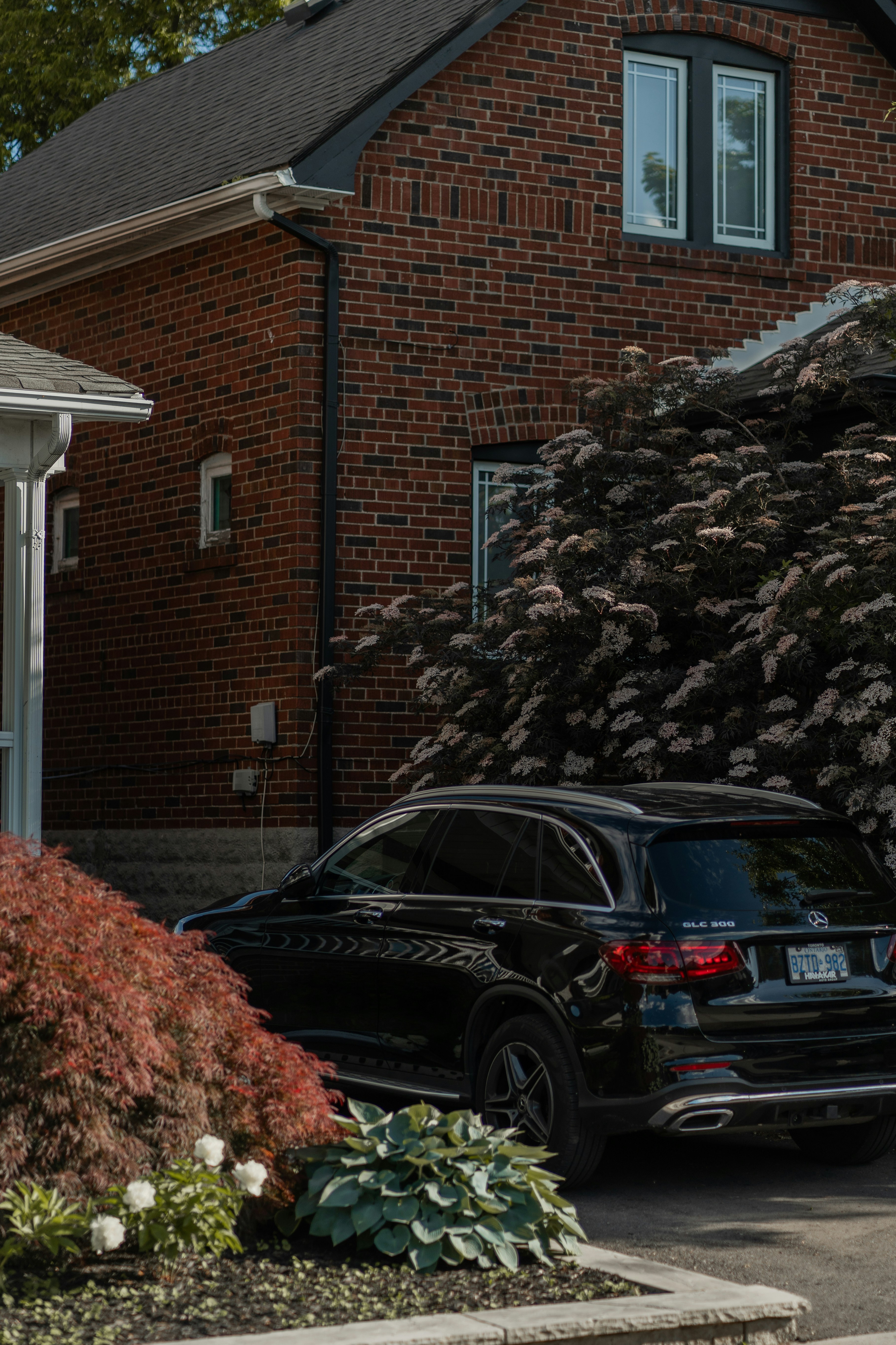 Suburban Quiet: Black SUV by Brick House and Blooming Garden
