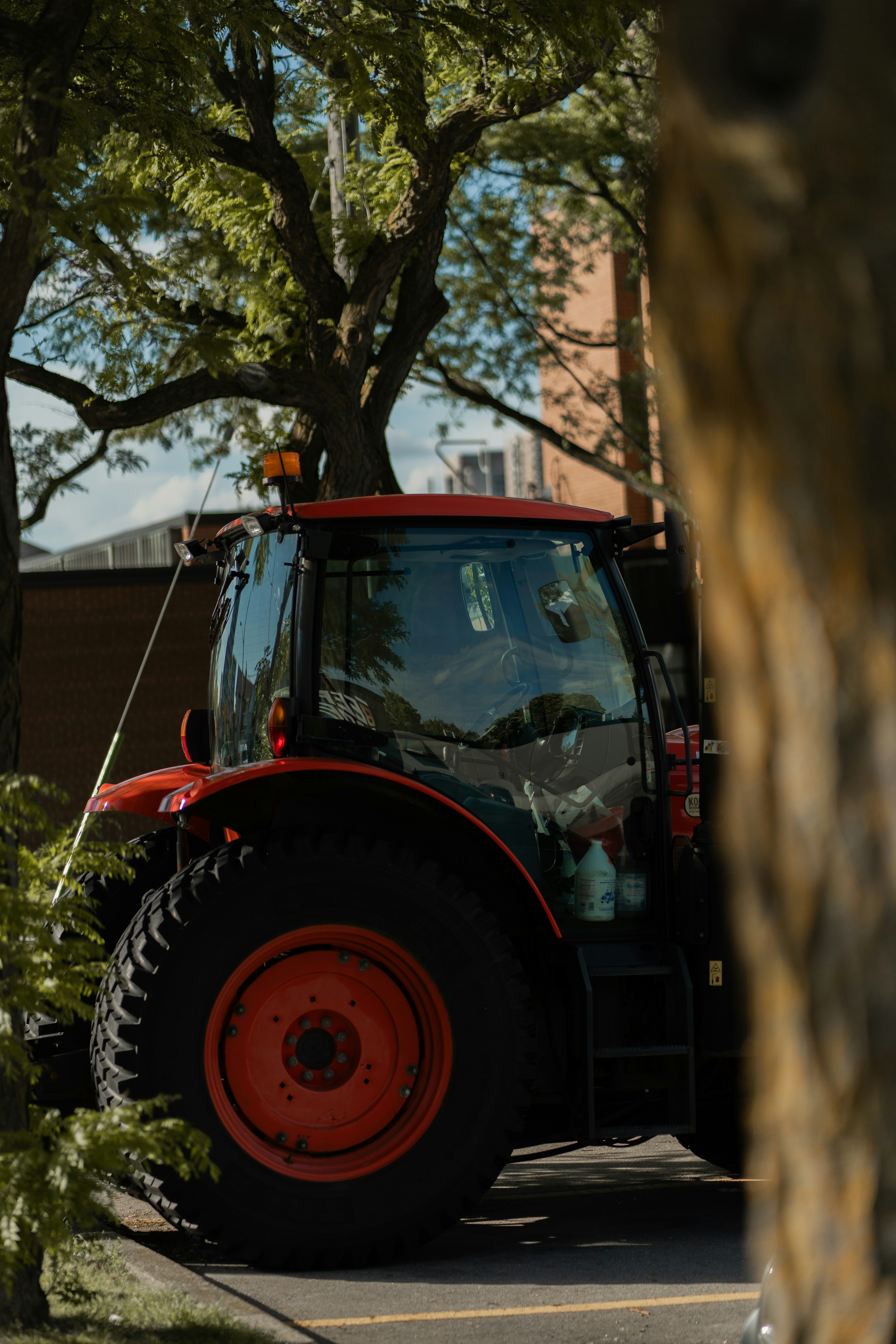 Under the Canopy: Red Tractor Resting in Shadowed Parking