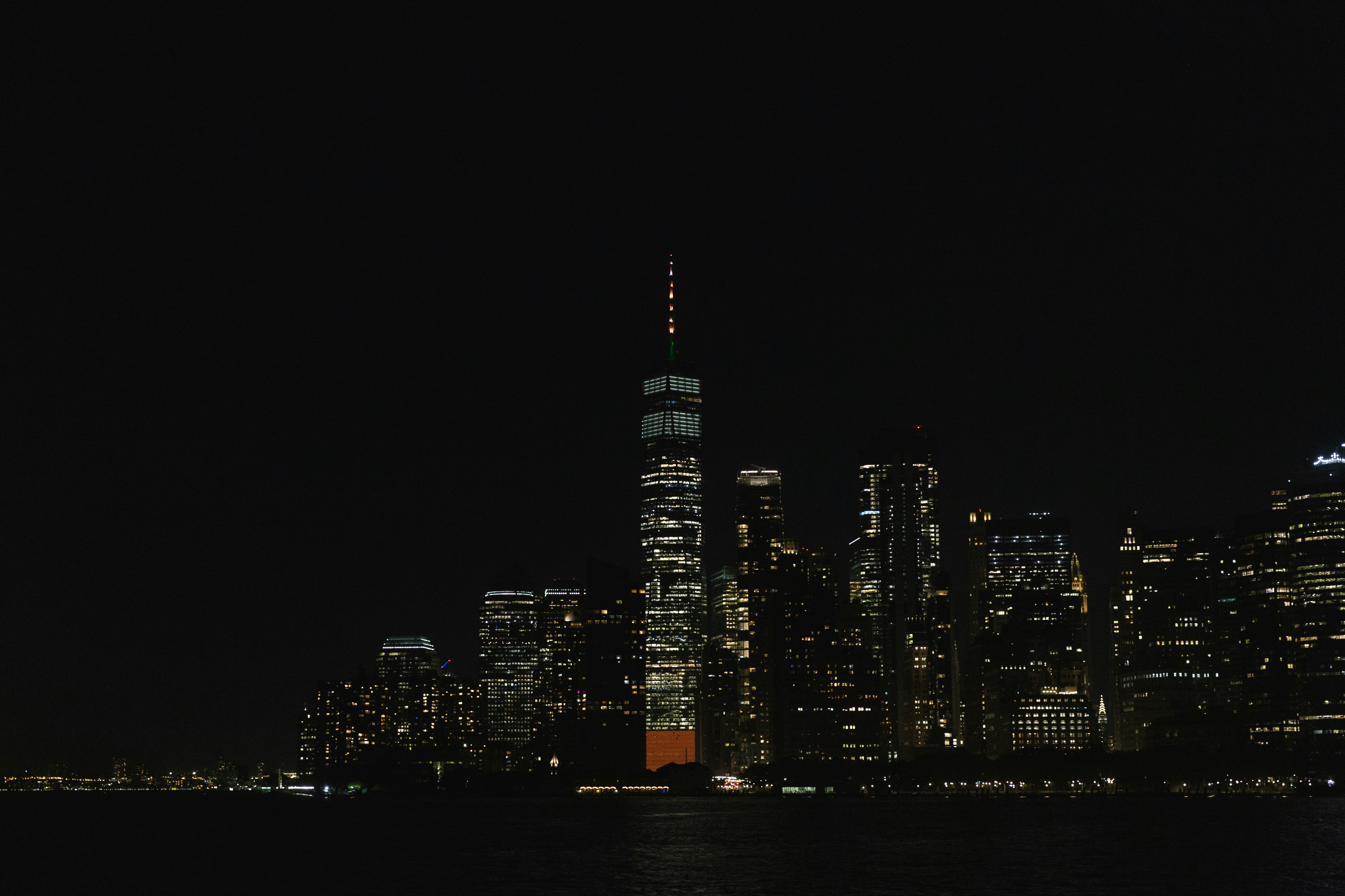 Illuminated skyline of a bustling city at night, showcasing towering skyscrapers and vibrant lights reflecting on the water.