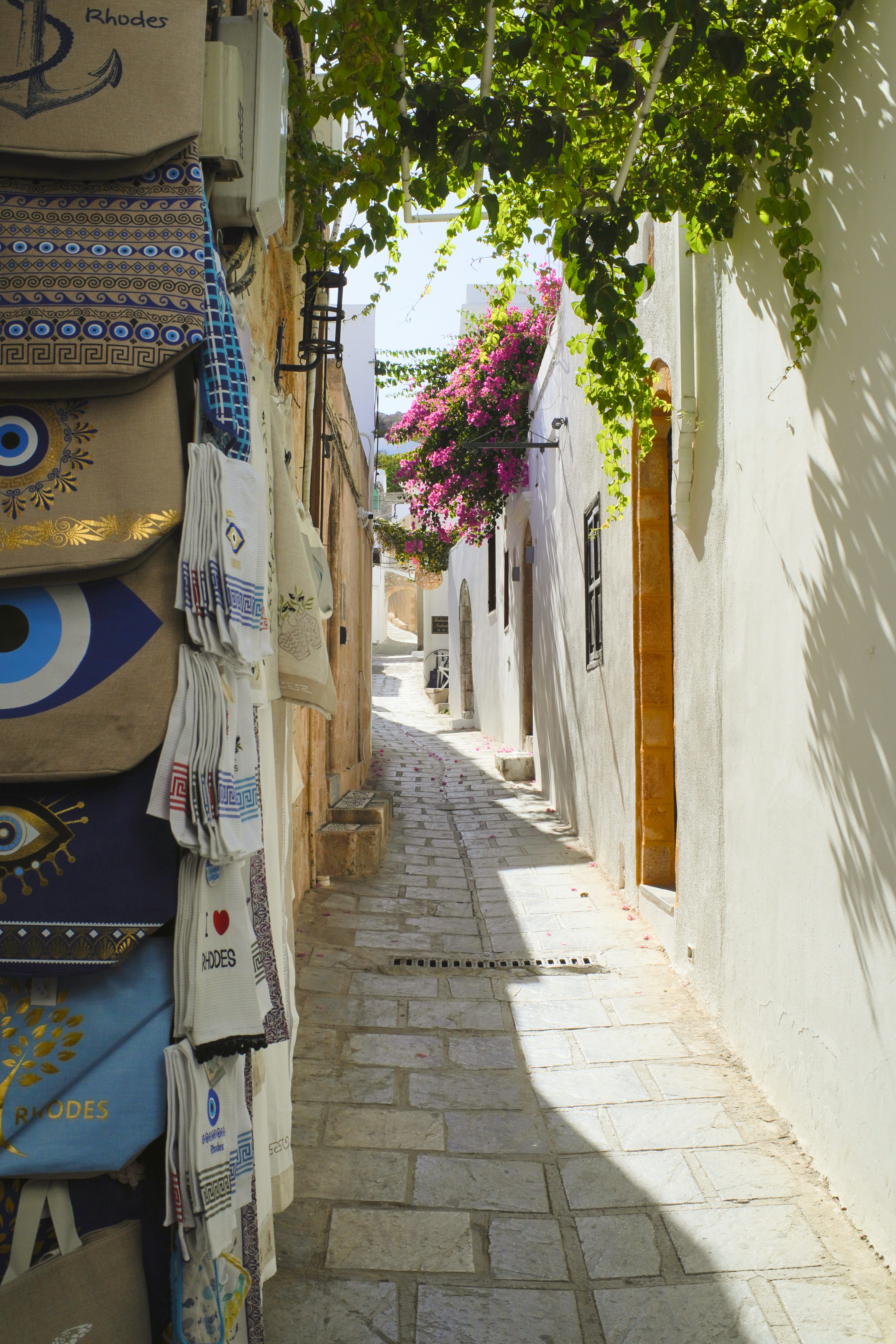 Sunlit Lanes: White-Walled Alley Framed by Textiles and Bougainvillea