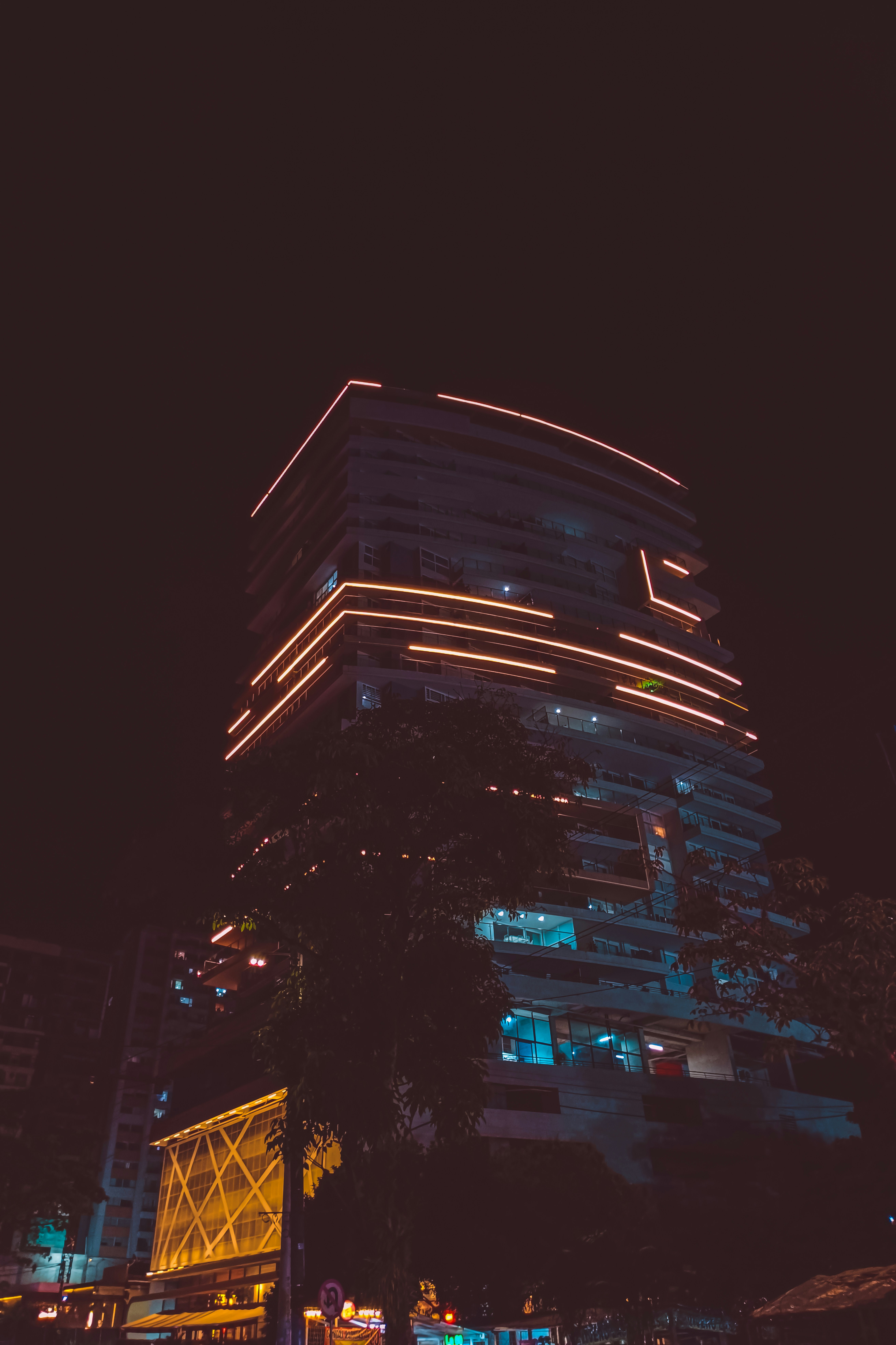 Night photograph of a tall high-rise outlined by warm neon lines, with blue-lit windows and a dim street below.
