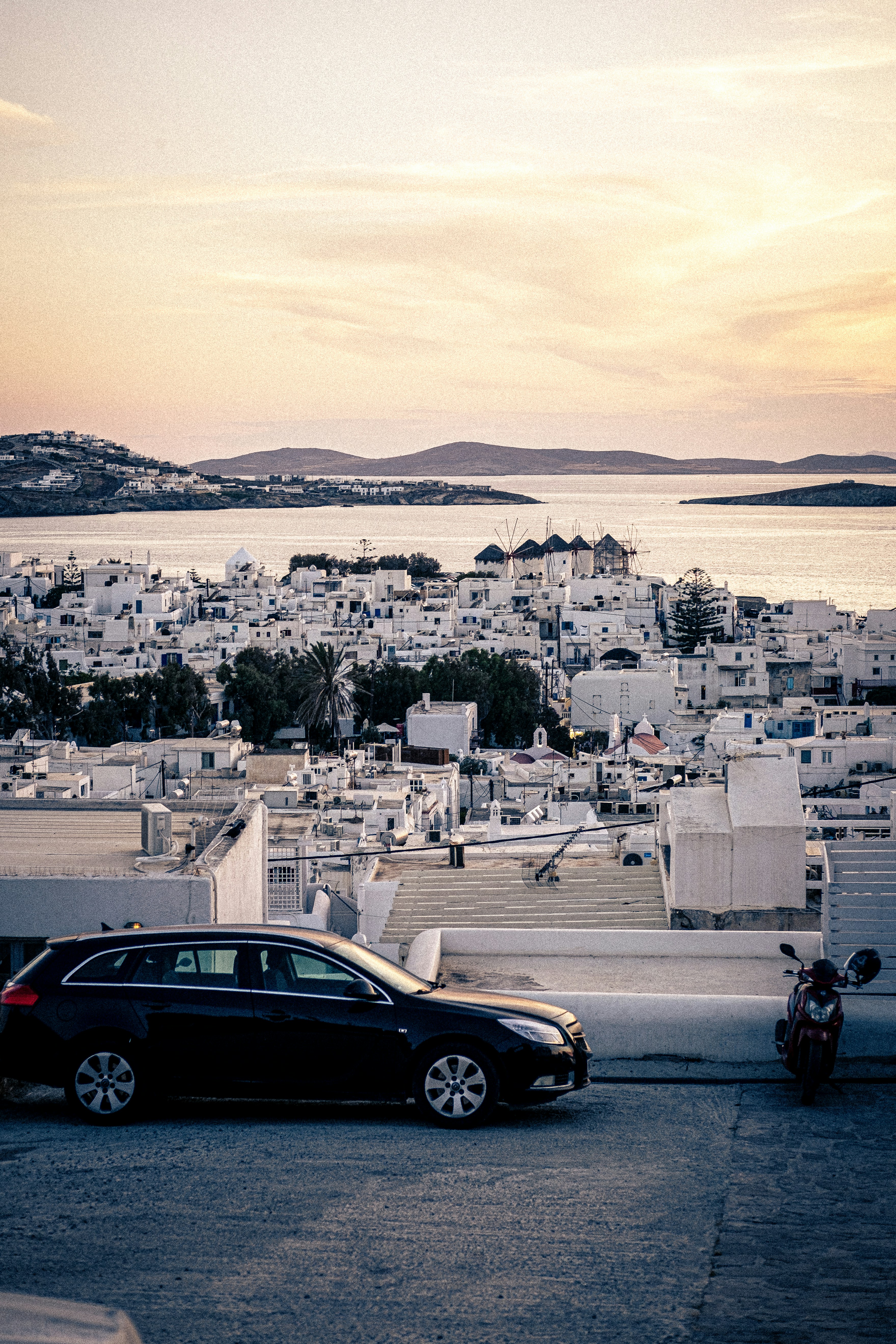 Golden Hour Over a Whitewashed Coastal Town: Car at the Promenade with Sea Horizons