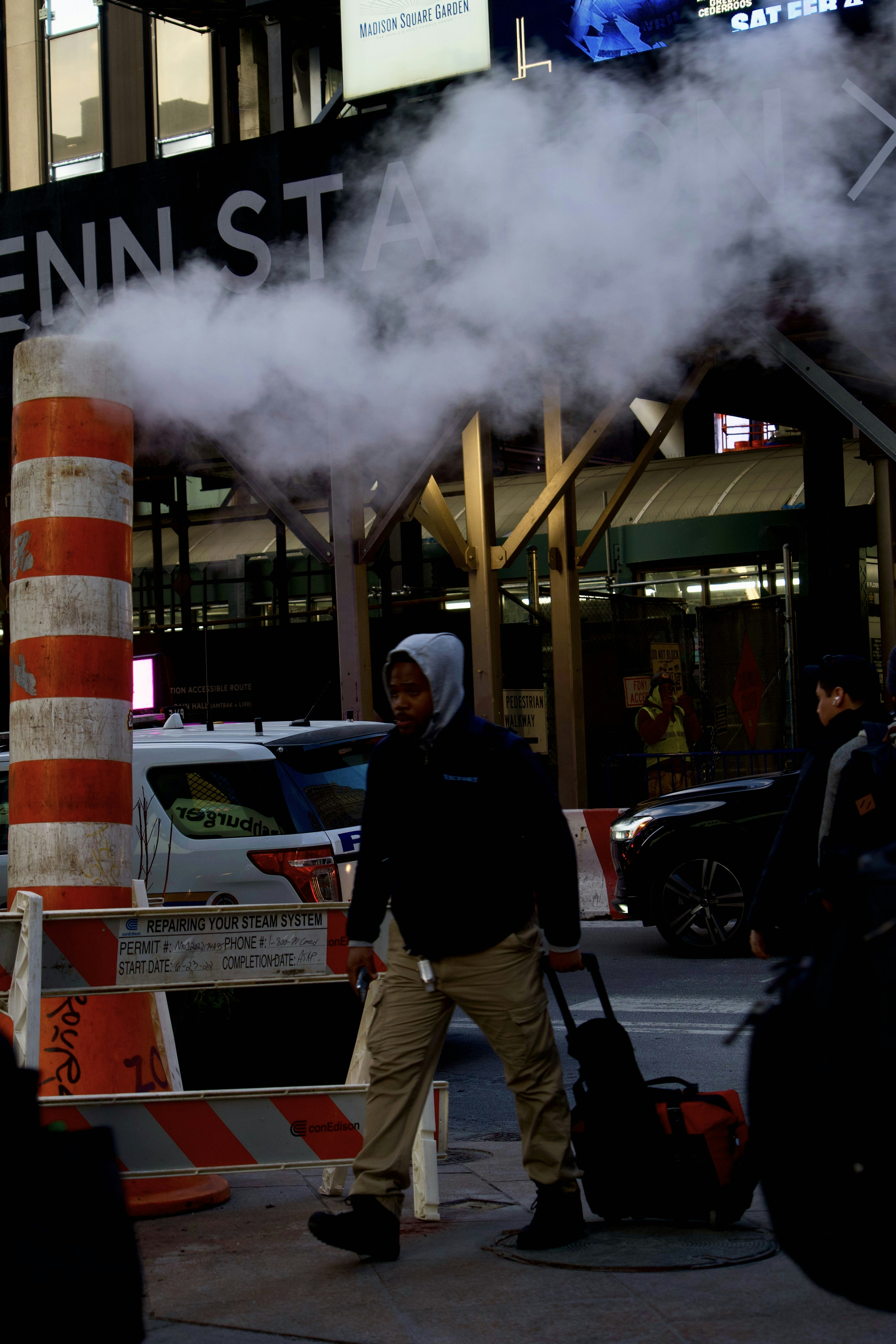 Urban routine under steam: a man with a hood near a construction plume