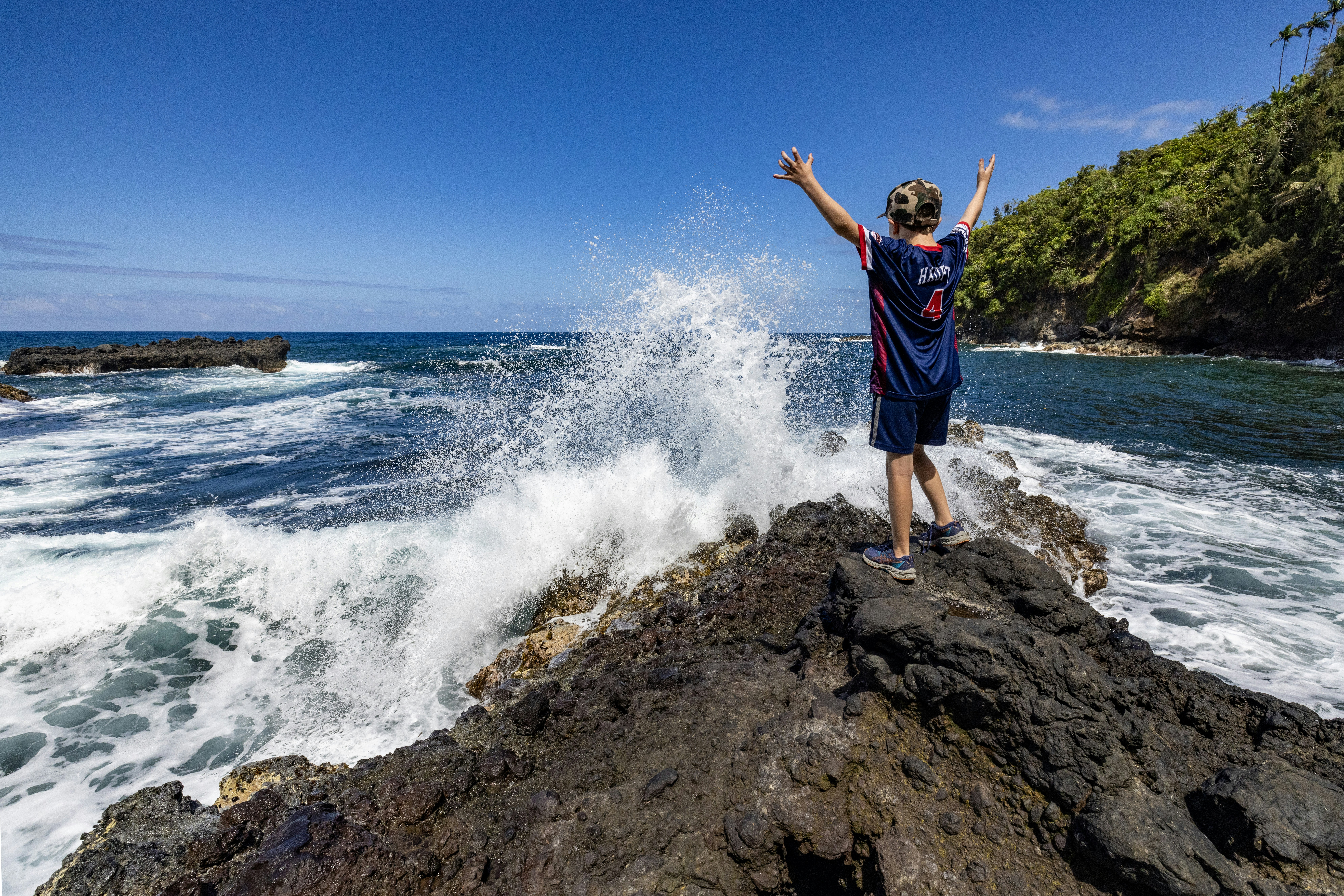 Edge of the Wave: A Boy Reaches Up on Craggy Coastal Rocks