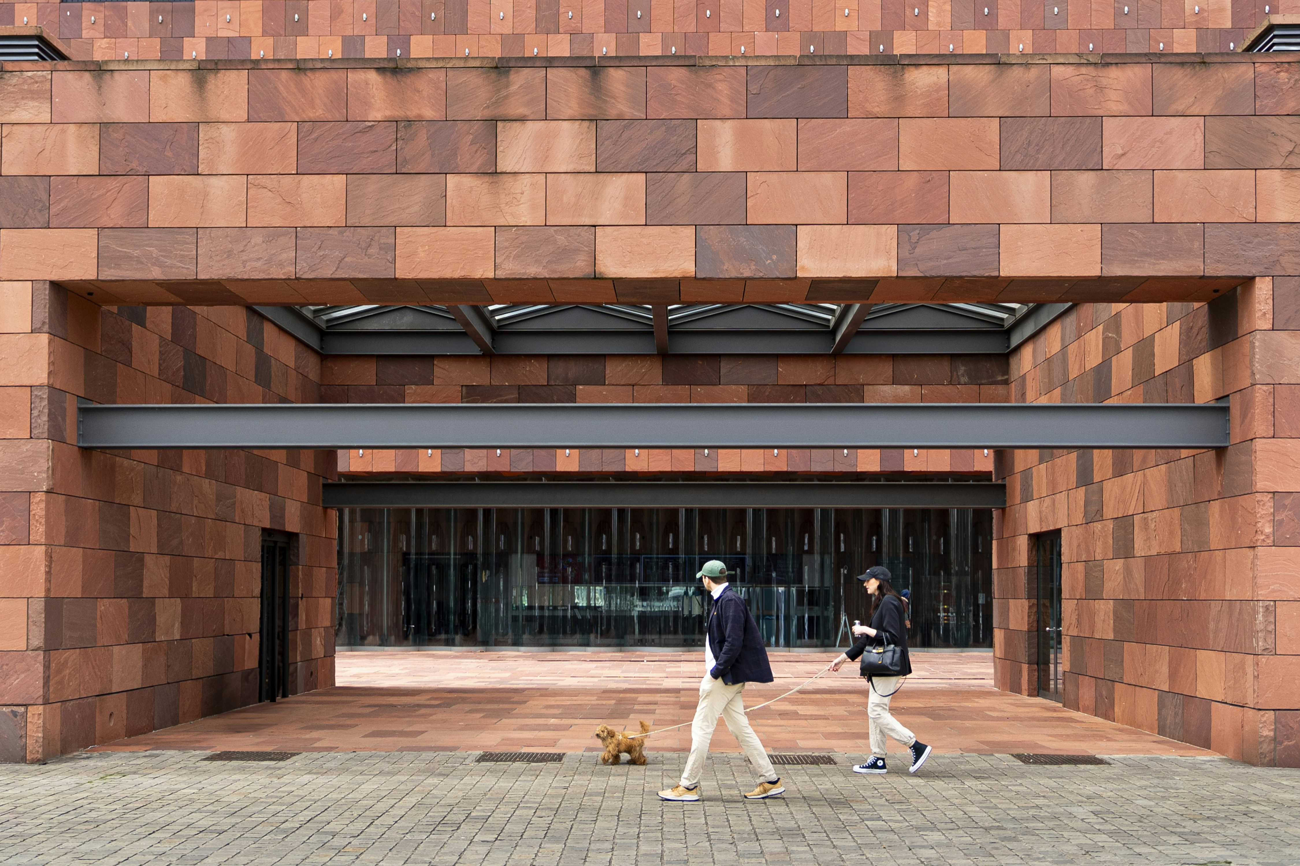Two people walking past a modern brick structure with geometric patterns.