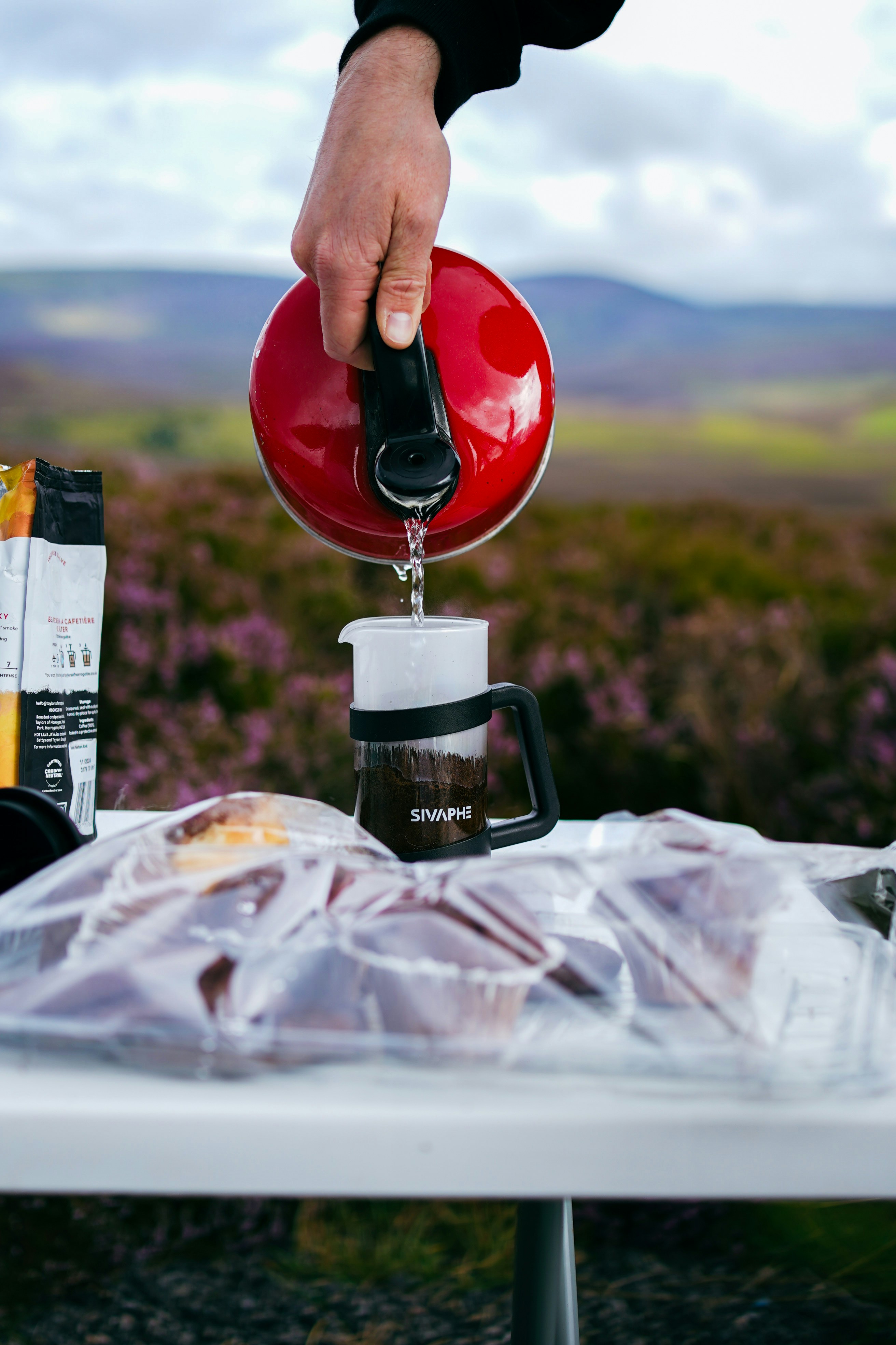 Pouring Outdoors: Red Kettle Over a Siphon Coffee Setup at a Rustic Picnic