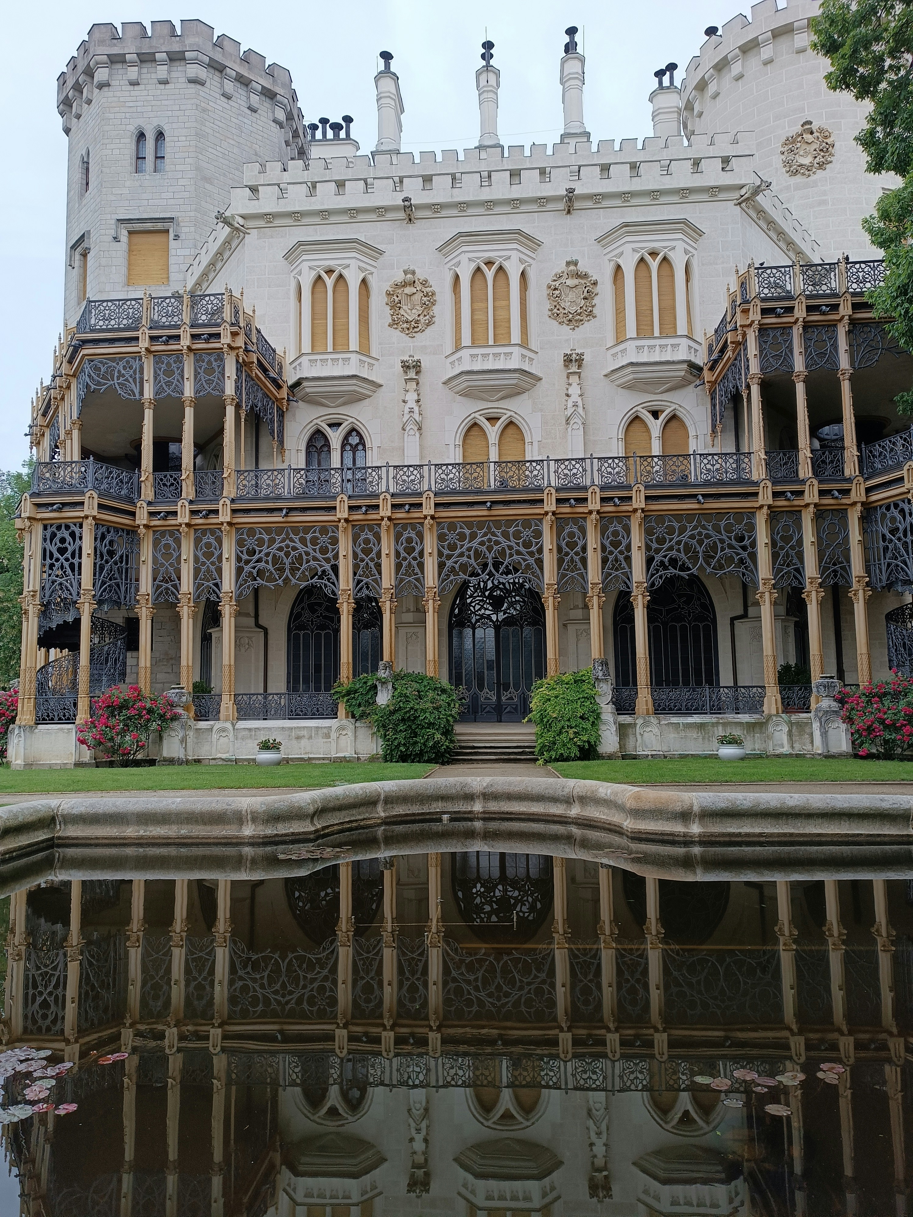 Historic mansion with ornate iron balconies, a carved stone facade, and a reflective pool that mirrors the architecture.