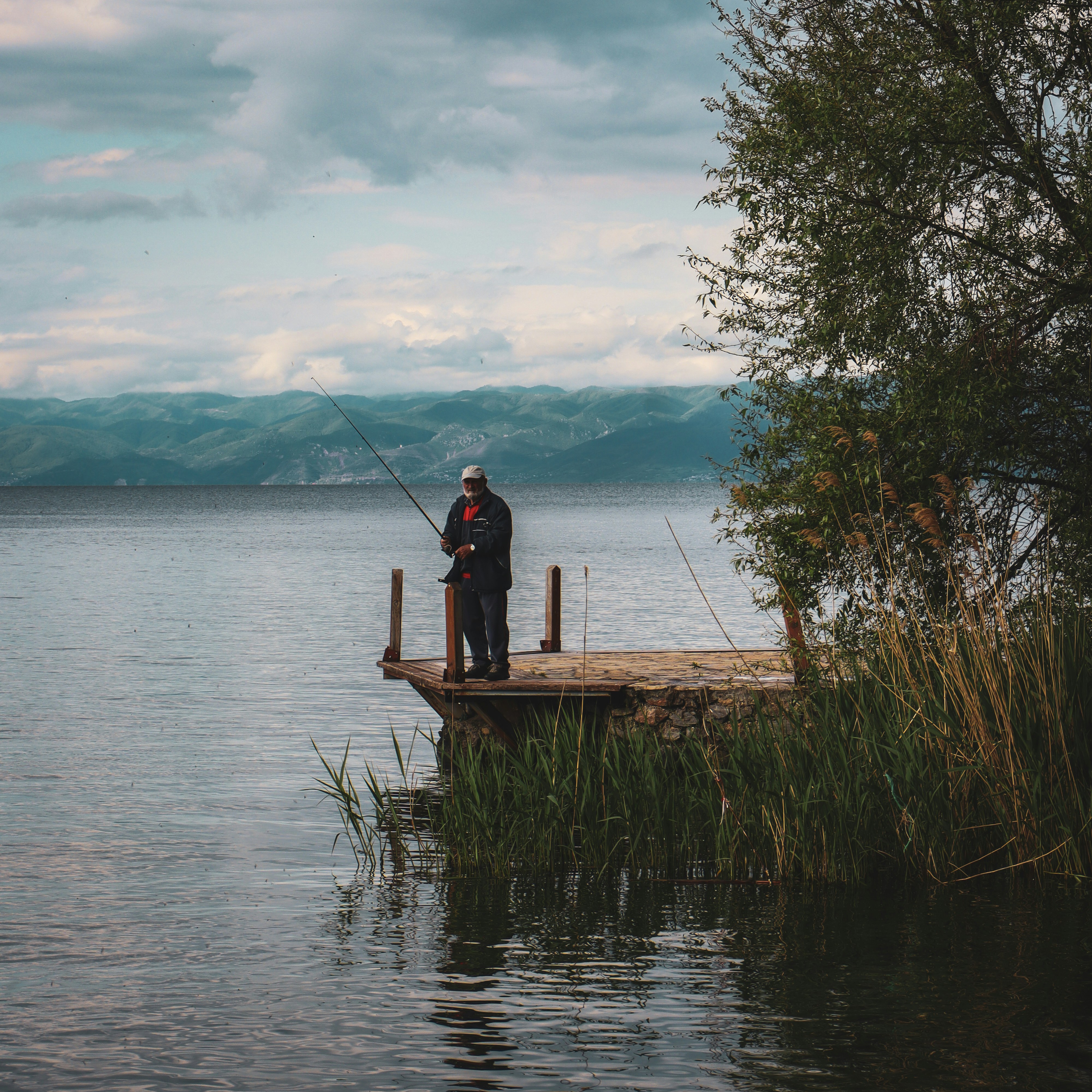A man standing on a dock next to a body of water photo – Free Fishman ...