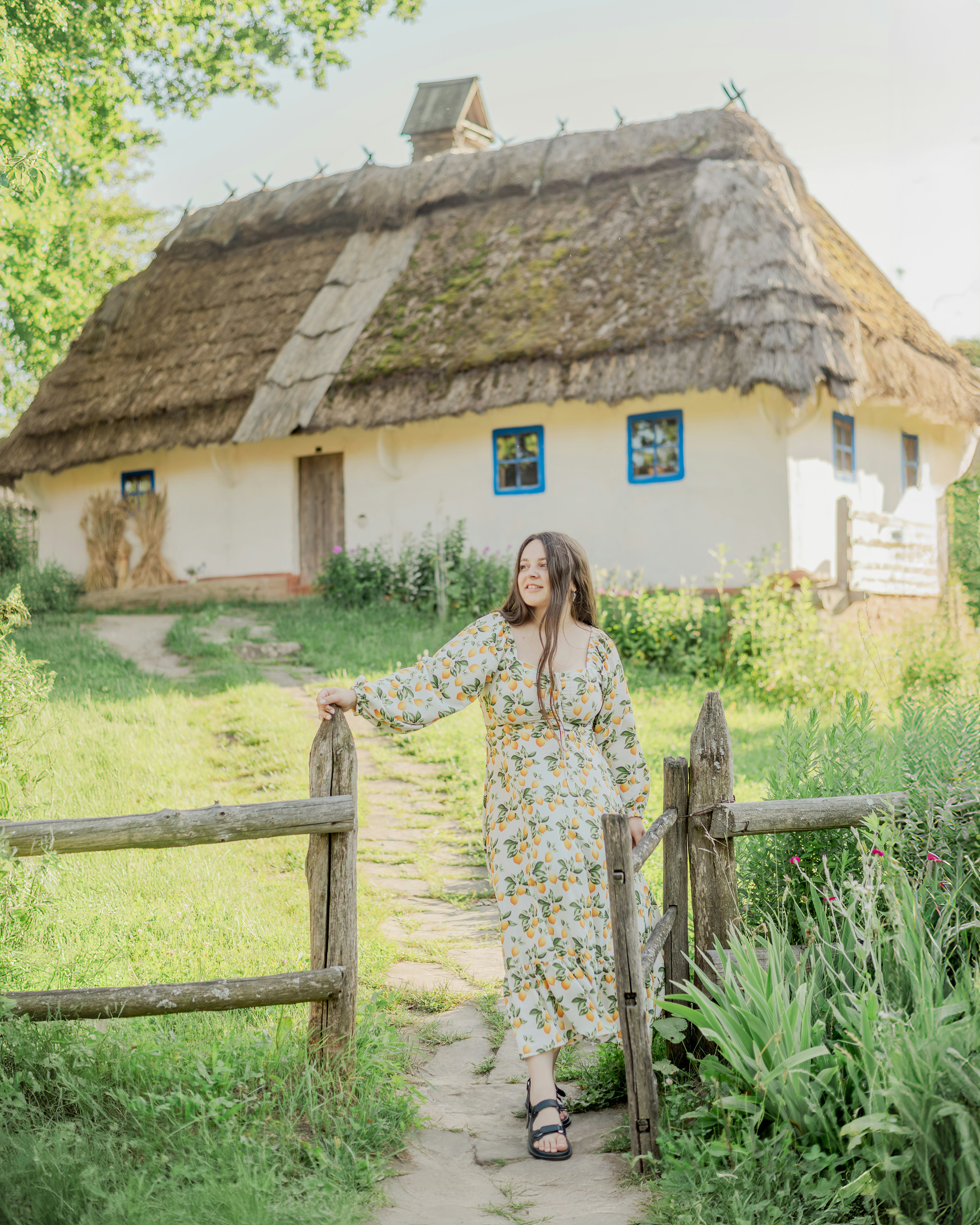 Sunlit Meadow Moment: A woman in a floral dress by a thatched cottage