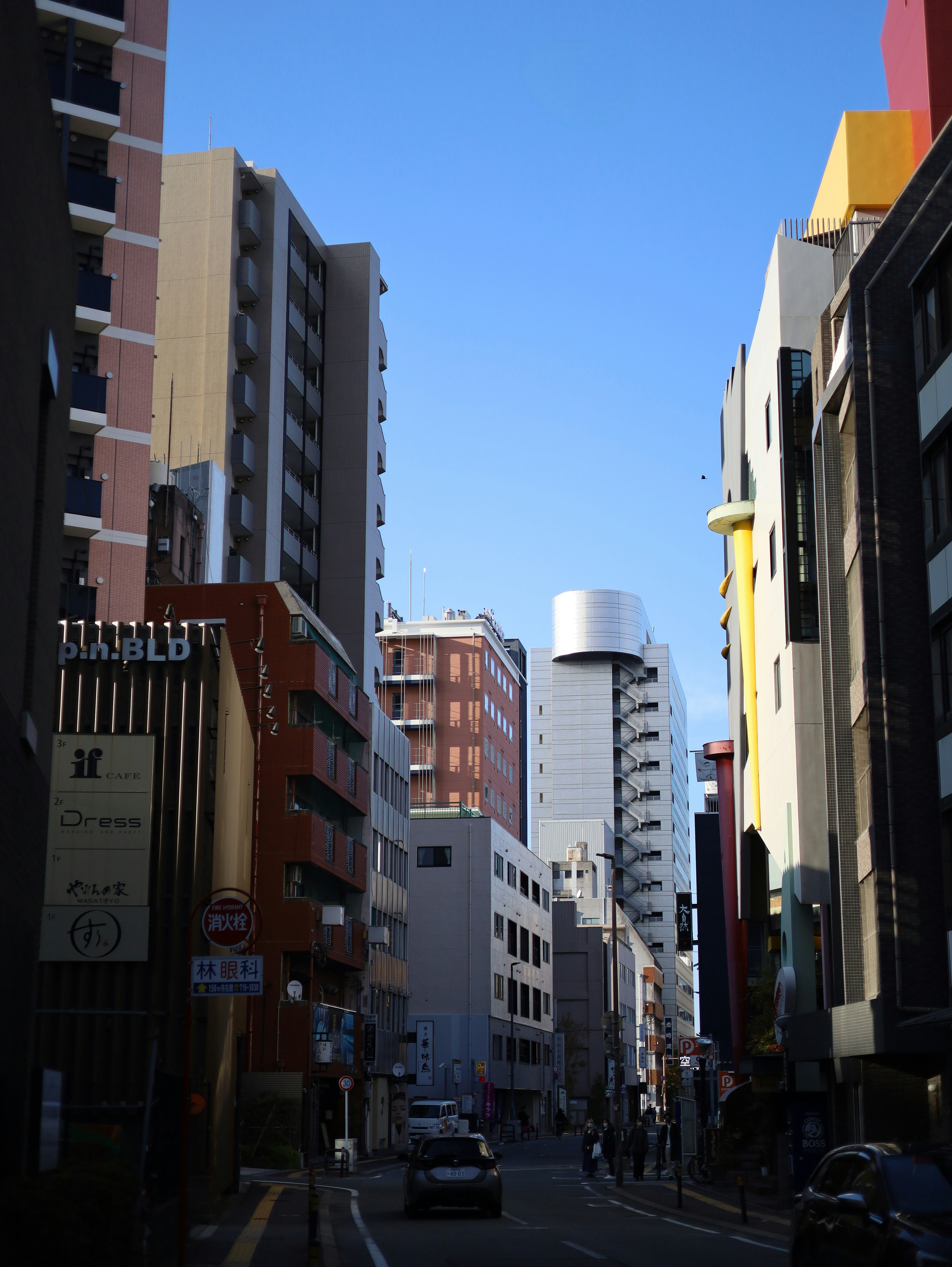 Narrow city street flanked by modern buildings, showcasing a blend of architectural styles and colors against a clear blue sky.