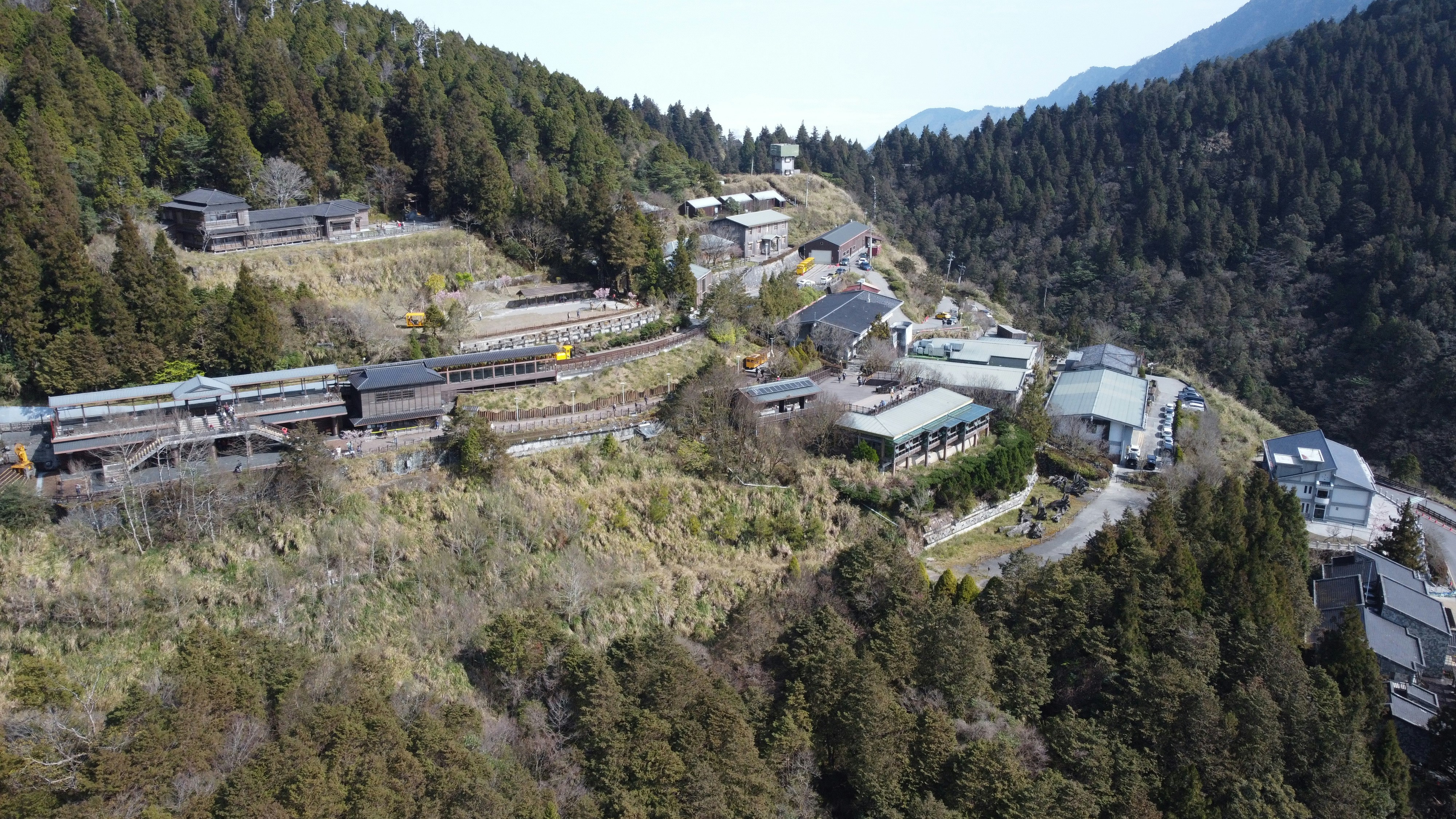 Aerial view of a hillside village surrounded by dense forest, showcasing a blend of modern architecture and natural landscape.