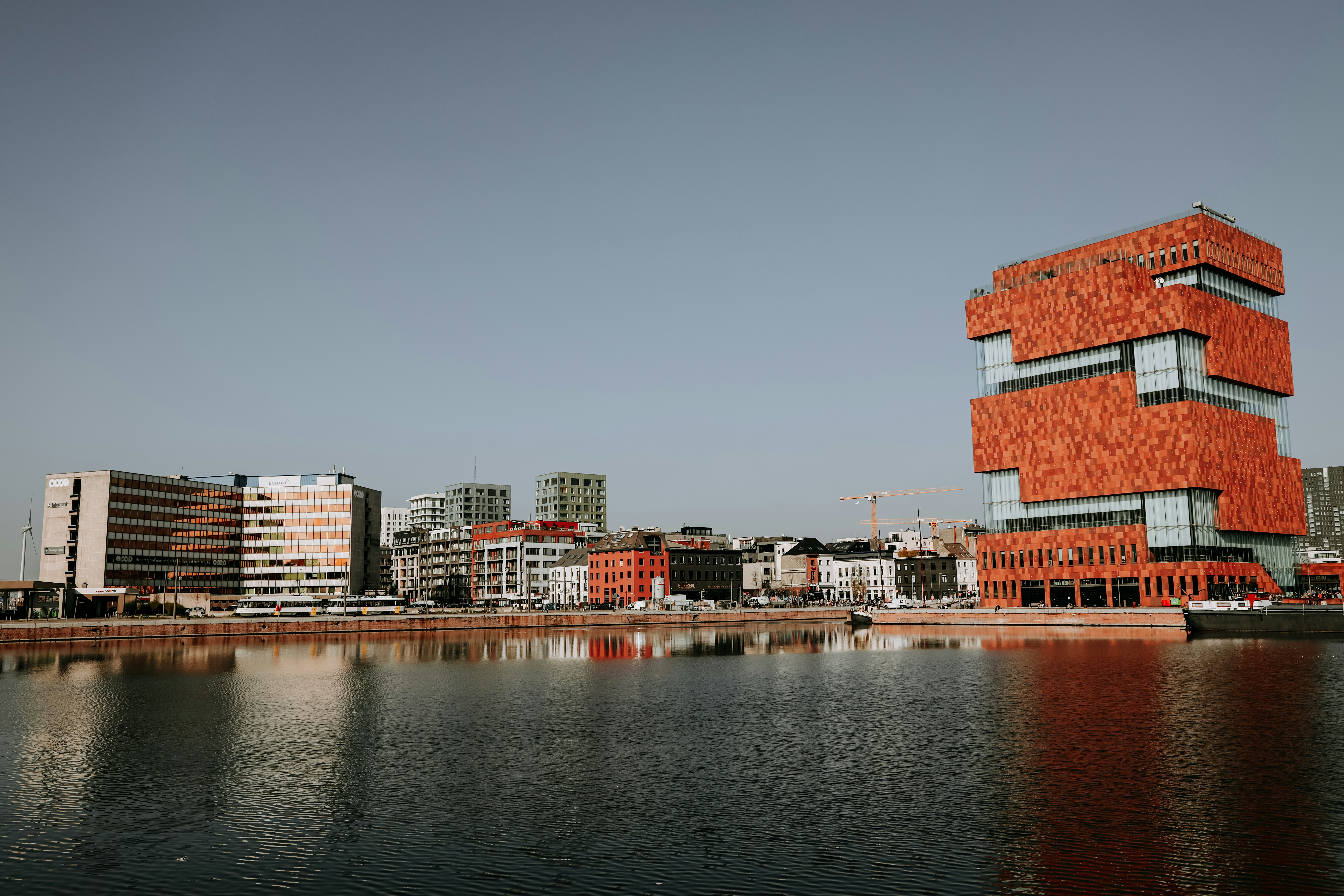 Unique red building with stacked design beside a tranquil urban waterfront.