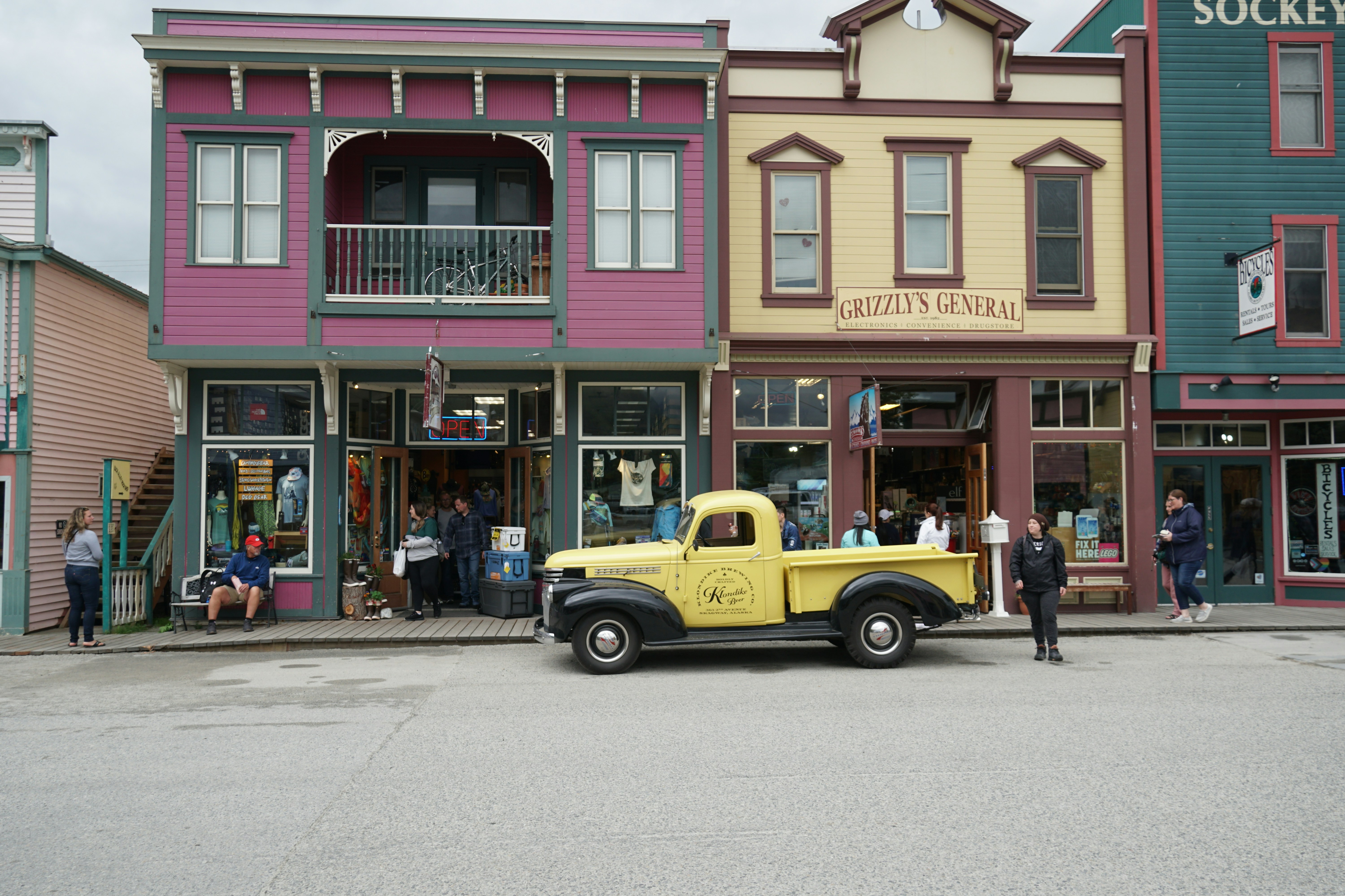 Yellow vintage pickup anchors a row of colorful storefronts in a quiet street