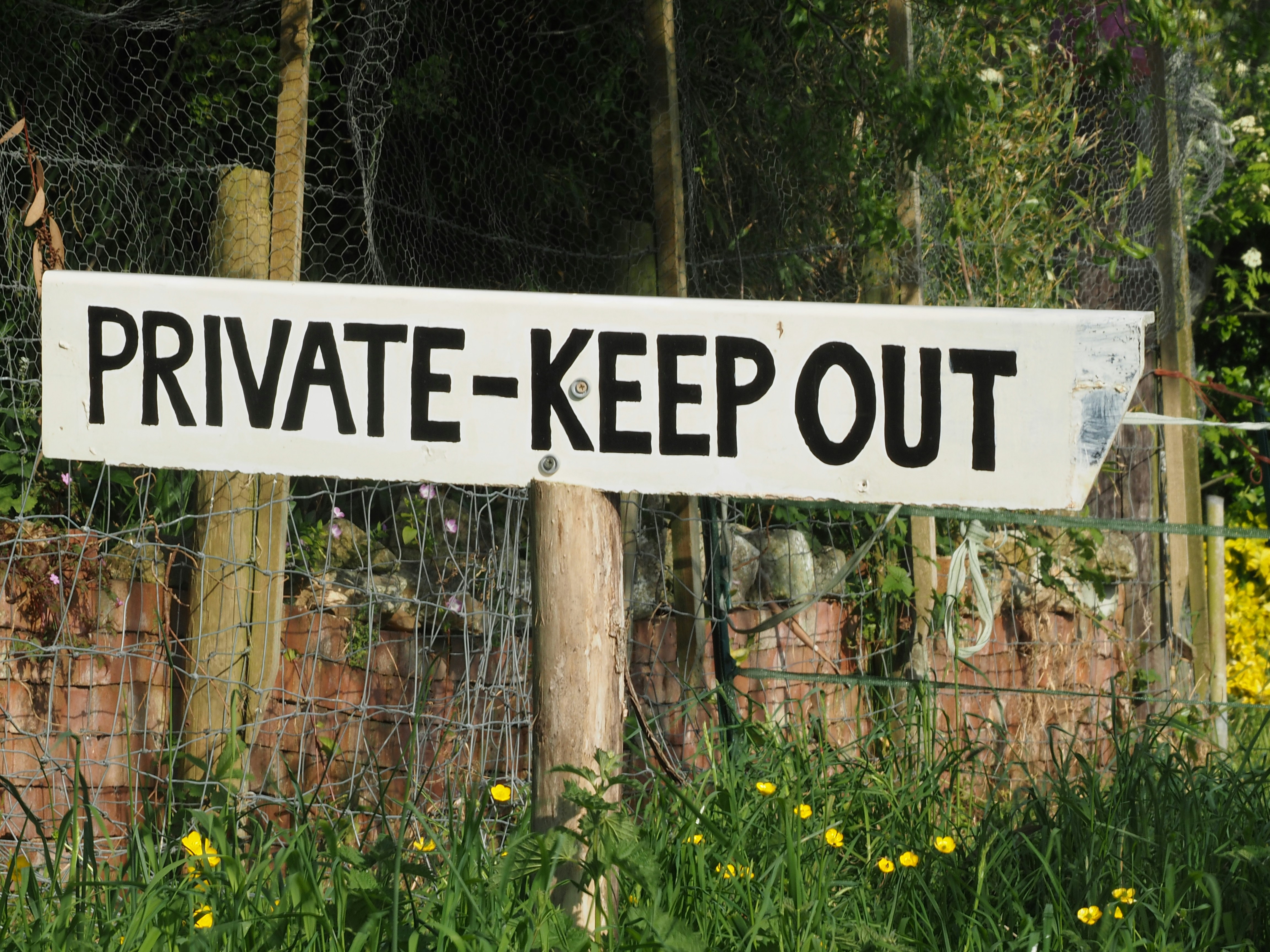 Bold sign declaring 'PRIVATE-KEEP OUT' positioned in a lush garden setting.