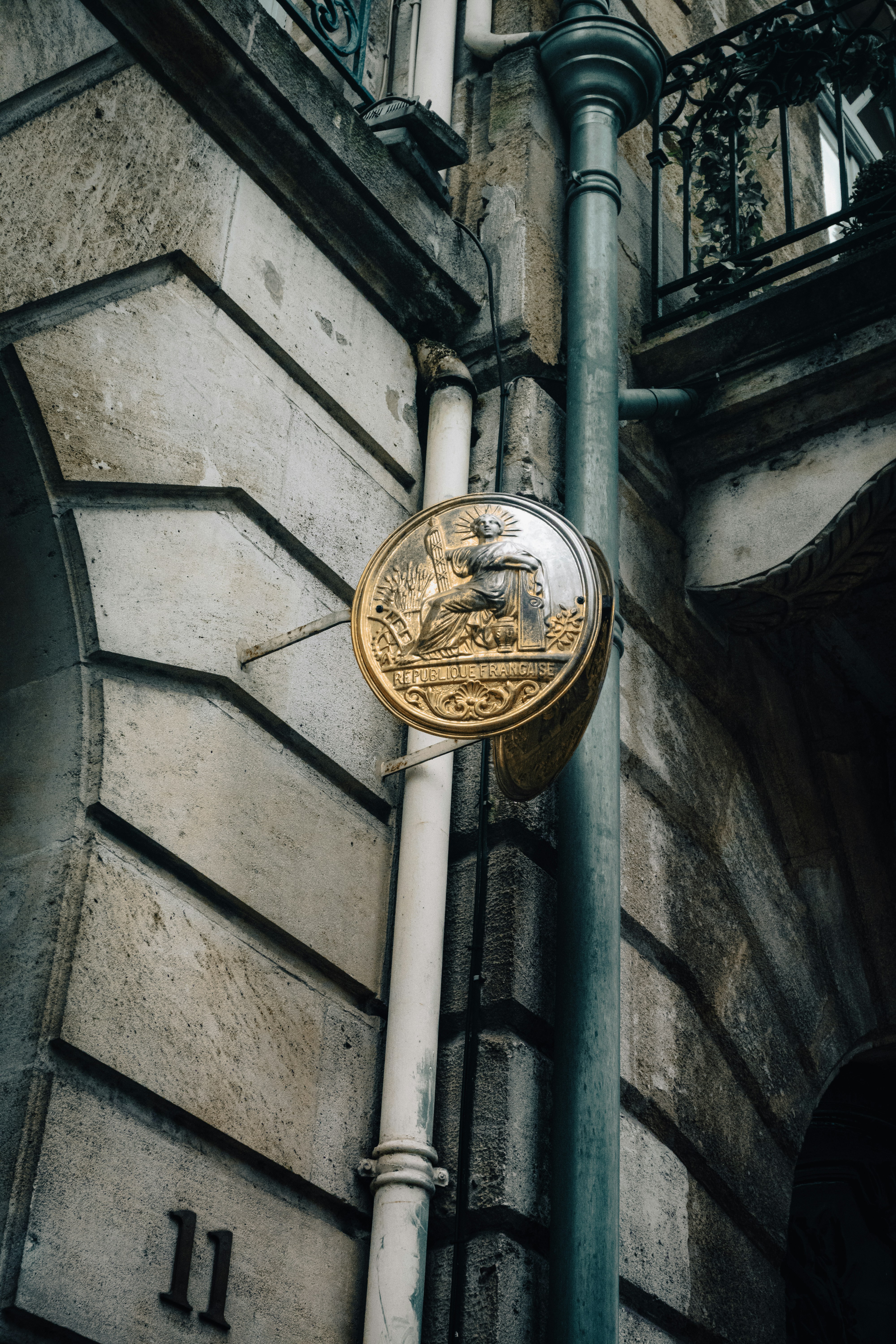 Brass Crest on a Timeworn Facade Beside Urban Piping