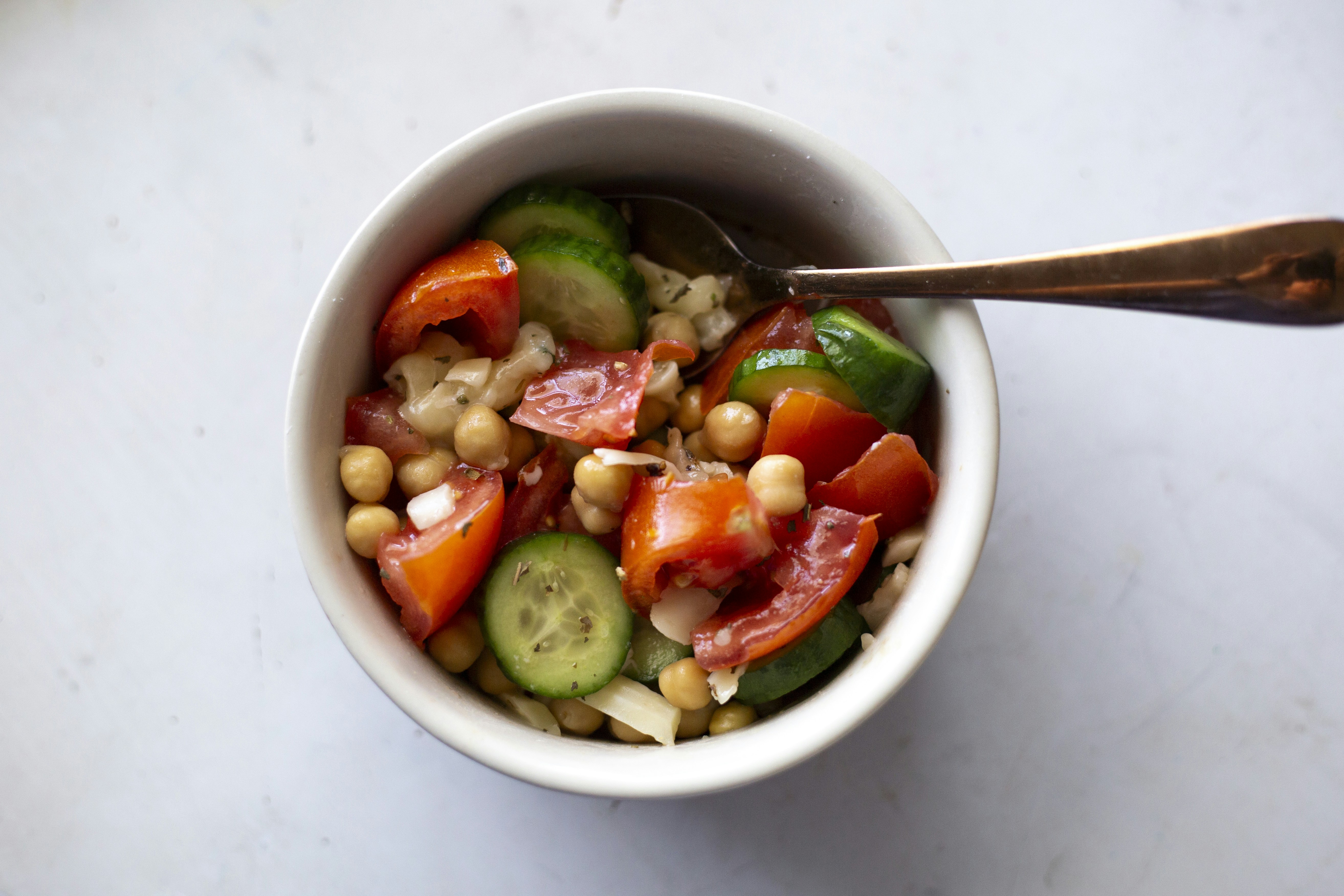 Garbanzo bean, cucumber, tomato salad in bowl with copper colored spoon
