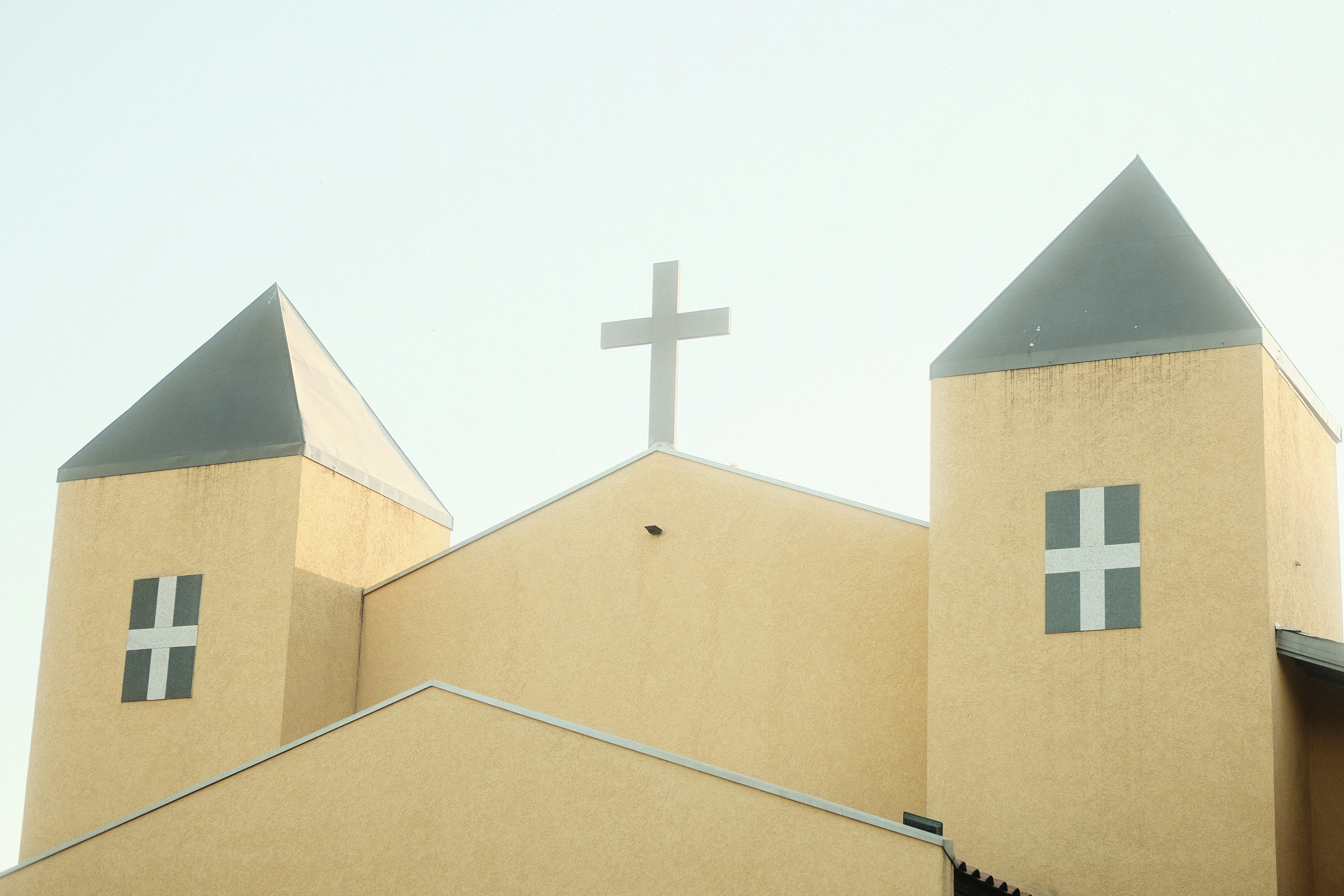 A modern church with a prominent cross atop its roof stands against a clear sky. The clean lines and geometric shapes of the building emphasize the simplicity and elegance of the design. The image evokes a sense of peace and tranquility, inviting contemplation and reflection.
