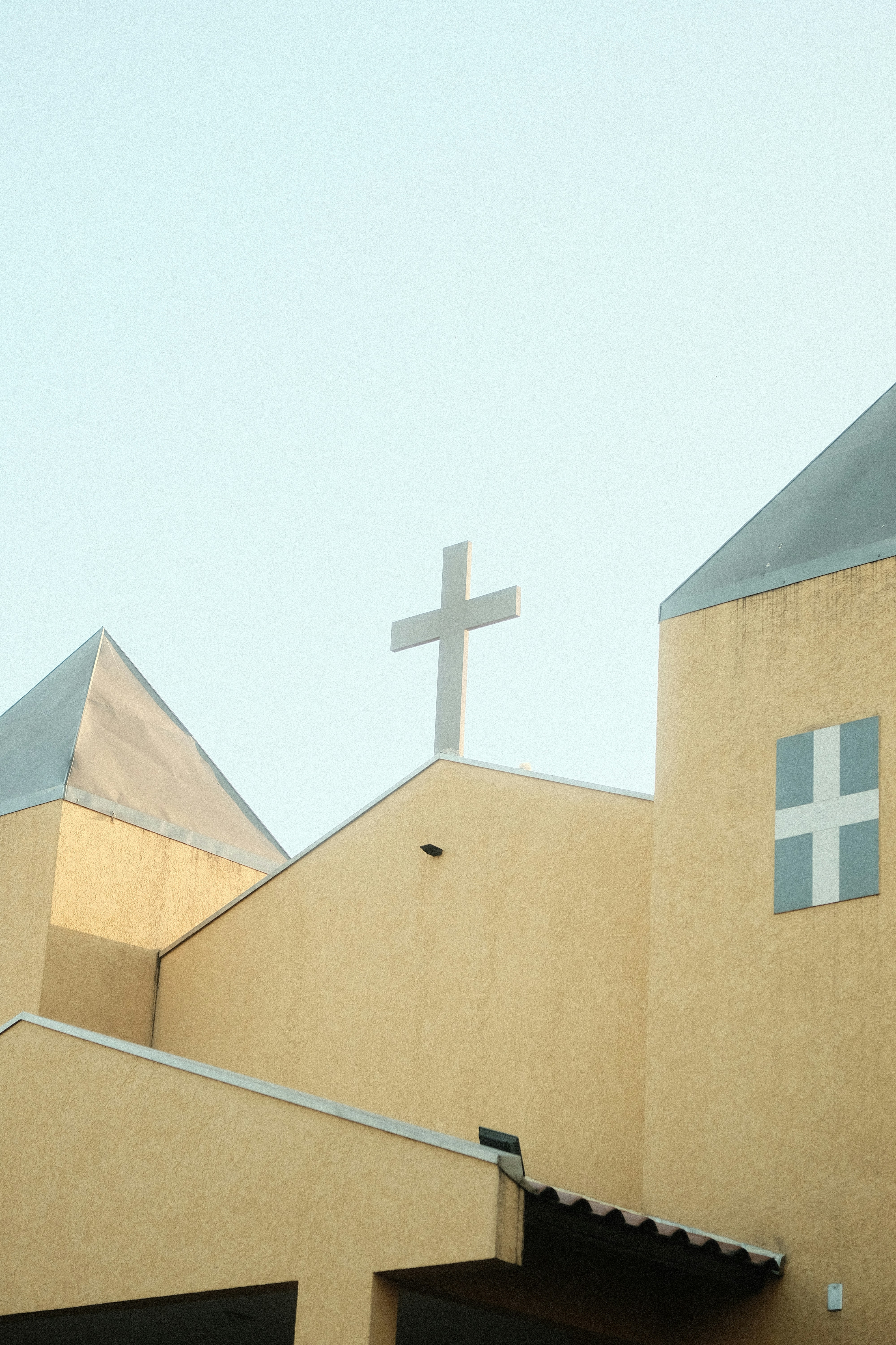 A modern church with a prominent cross atop its roof stands against a clear sky. The clean lines and geometric shapes of the building emphasize the simplicity and elegance of the design. The image evokes a sense of peace and tranquility, inviting contemplation and reflection.