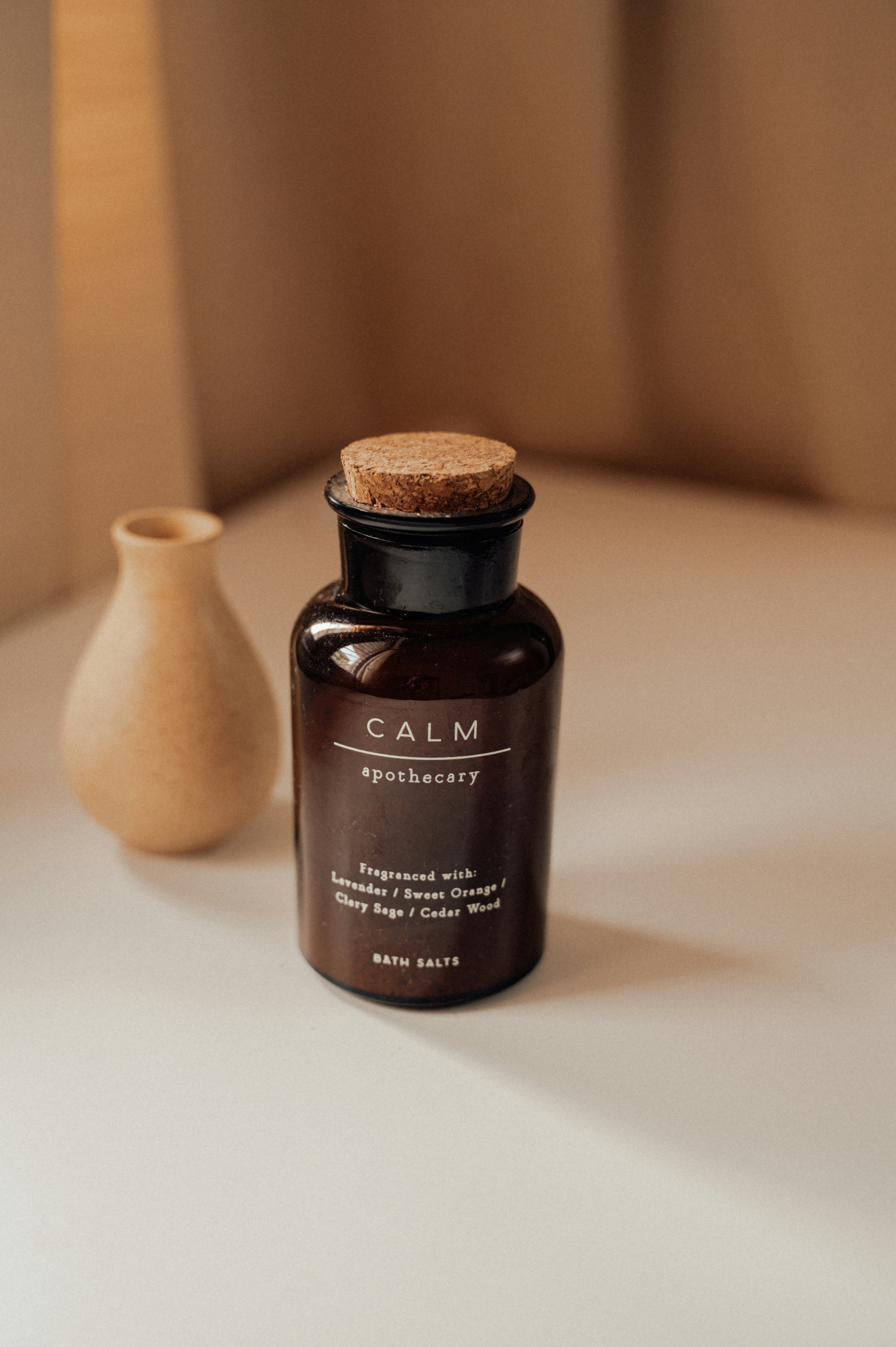 A bottle of calm on a table next to a vaseMona Jain