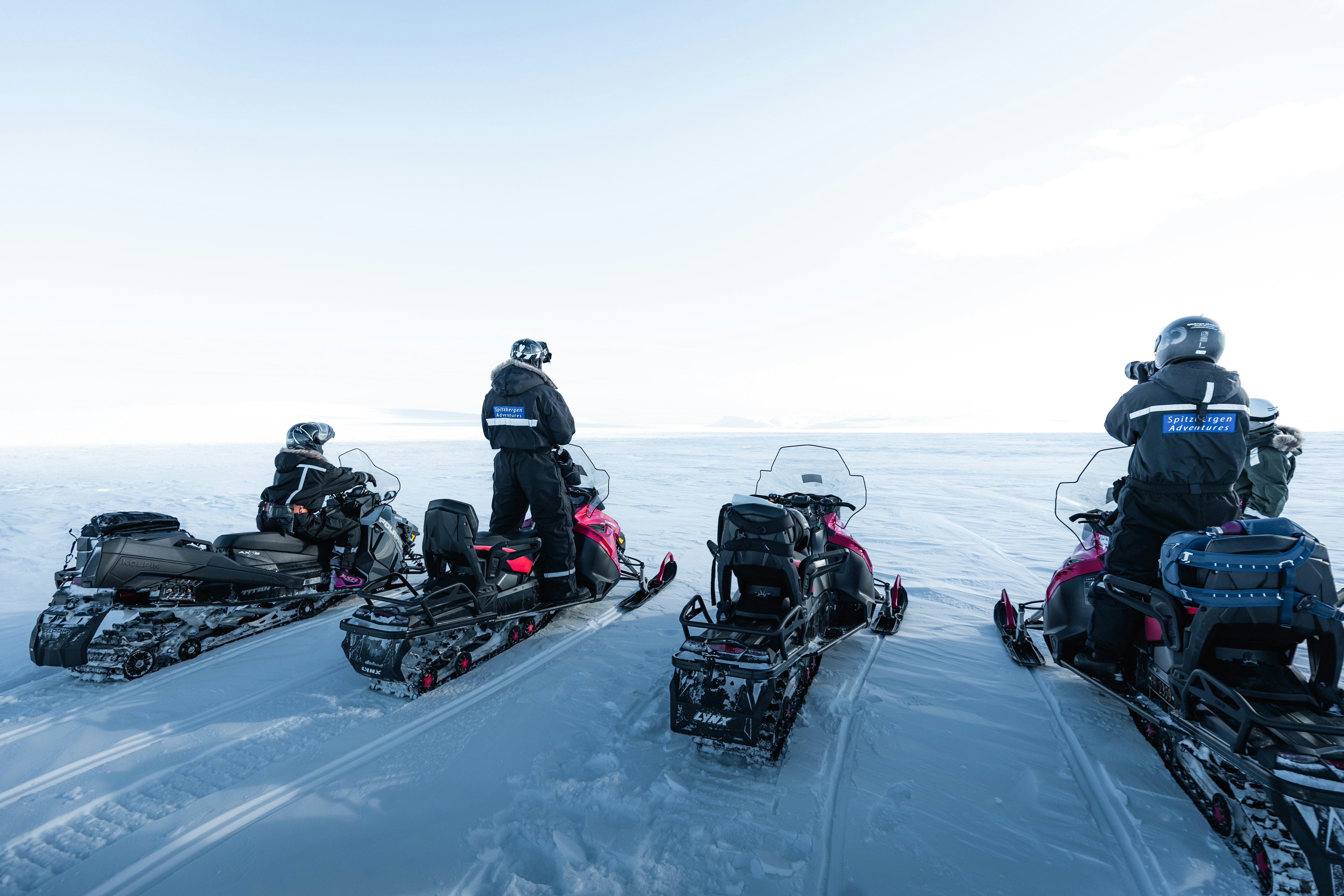 A group of people riding snowmobiles on top of a snow covered slope ...