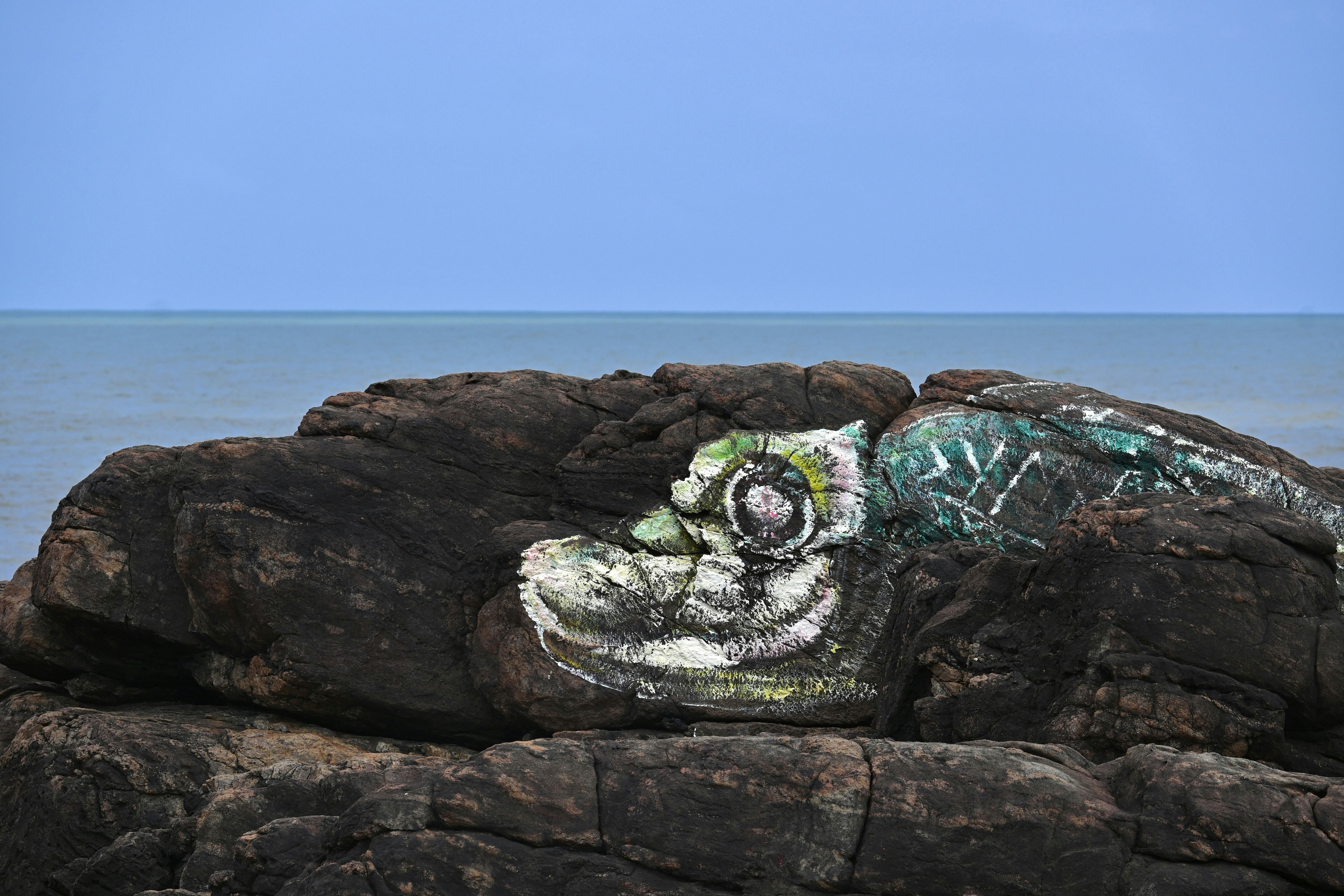 Shoreline Portrait: Weathered Rock Graffiti Between Sea and Sky