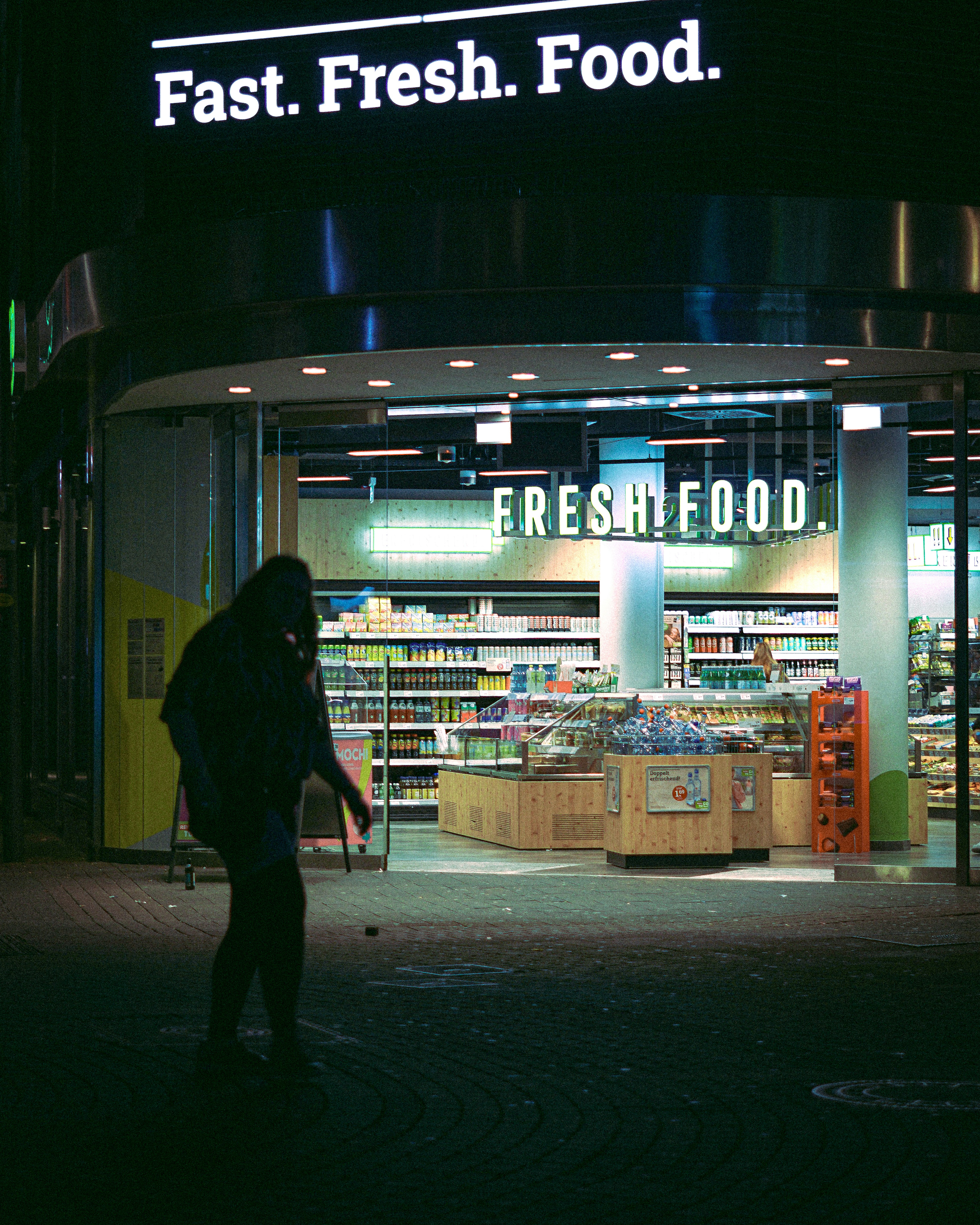 Neon Threshold: Nighttime Grocery Glow Behind a Dark Silhouette