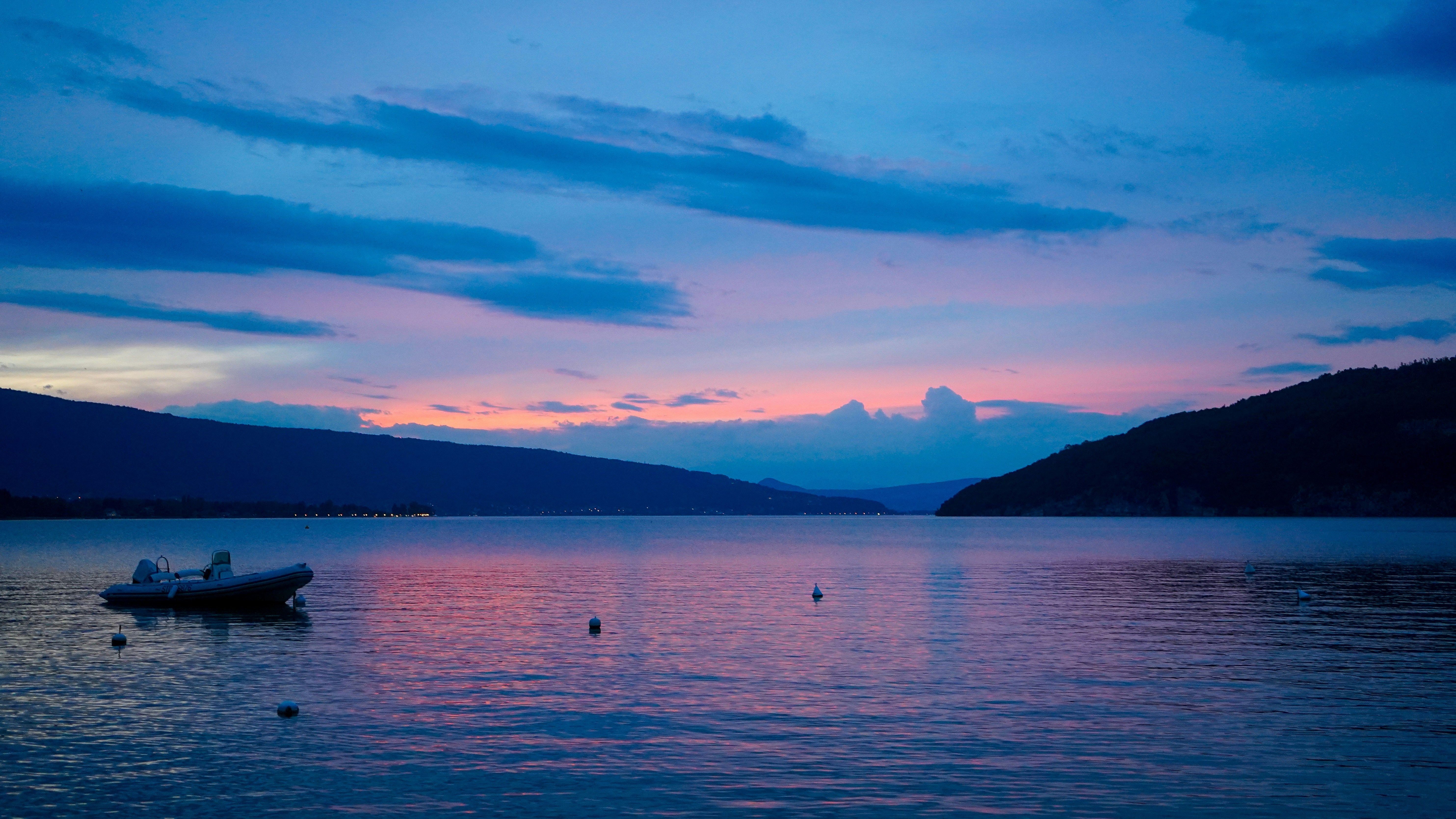 Boat floating on Lake Annecy with vibrant pink and blue sunset hues in the sky.