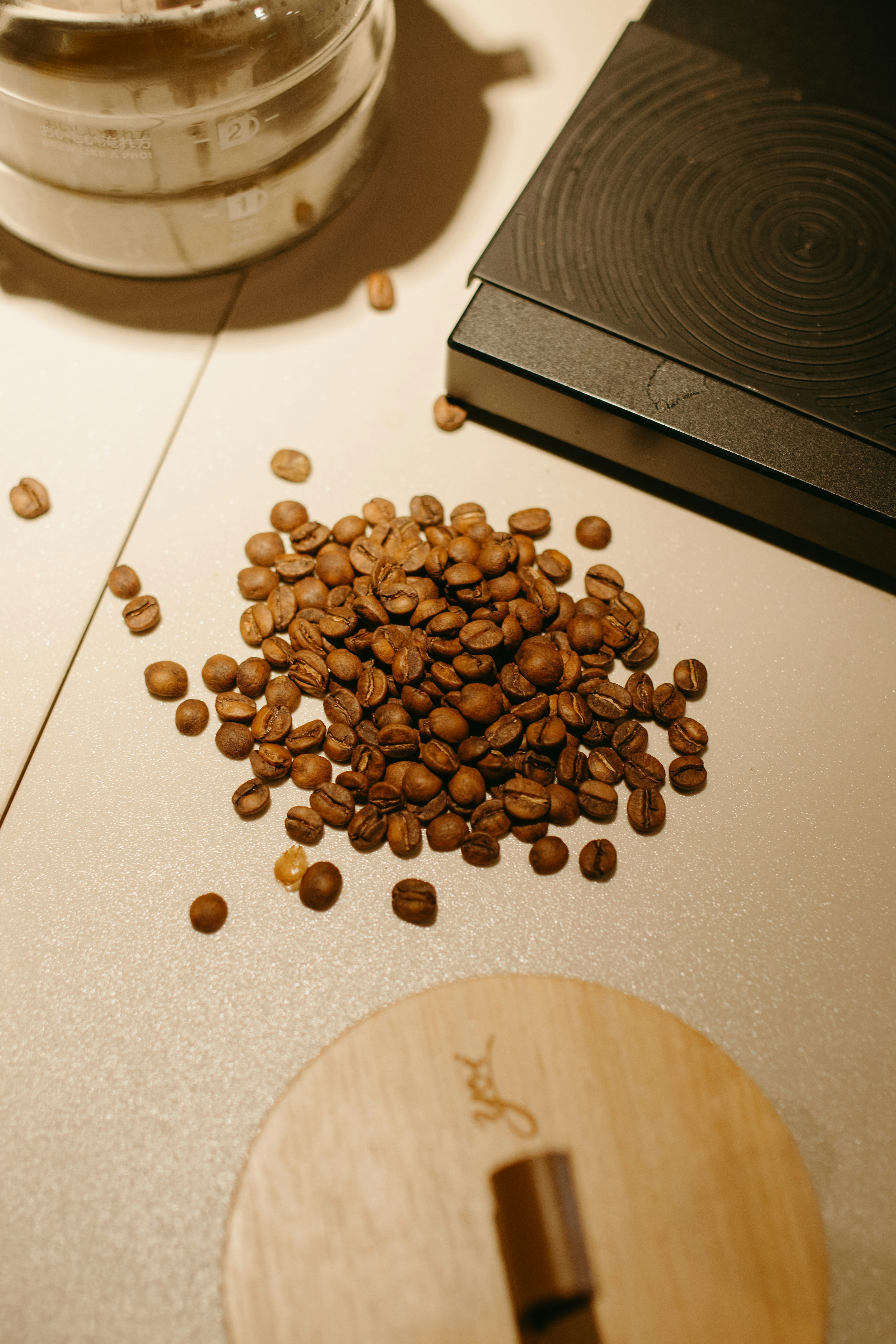 Quiet Scatter: Roasted Coffee Beans Beside a Manual Grinder on a Light Counter
