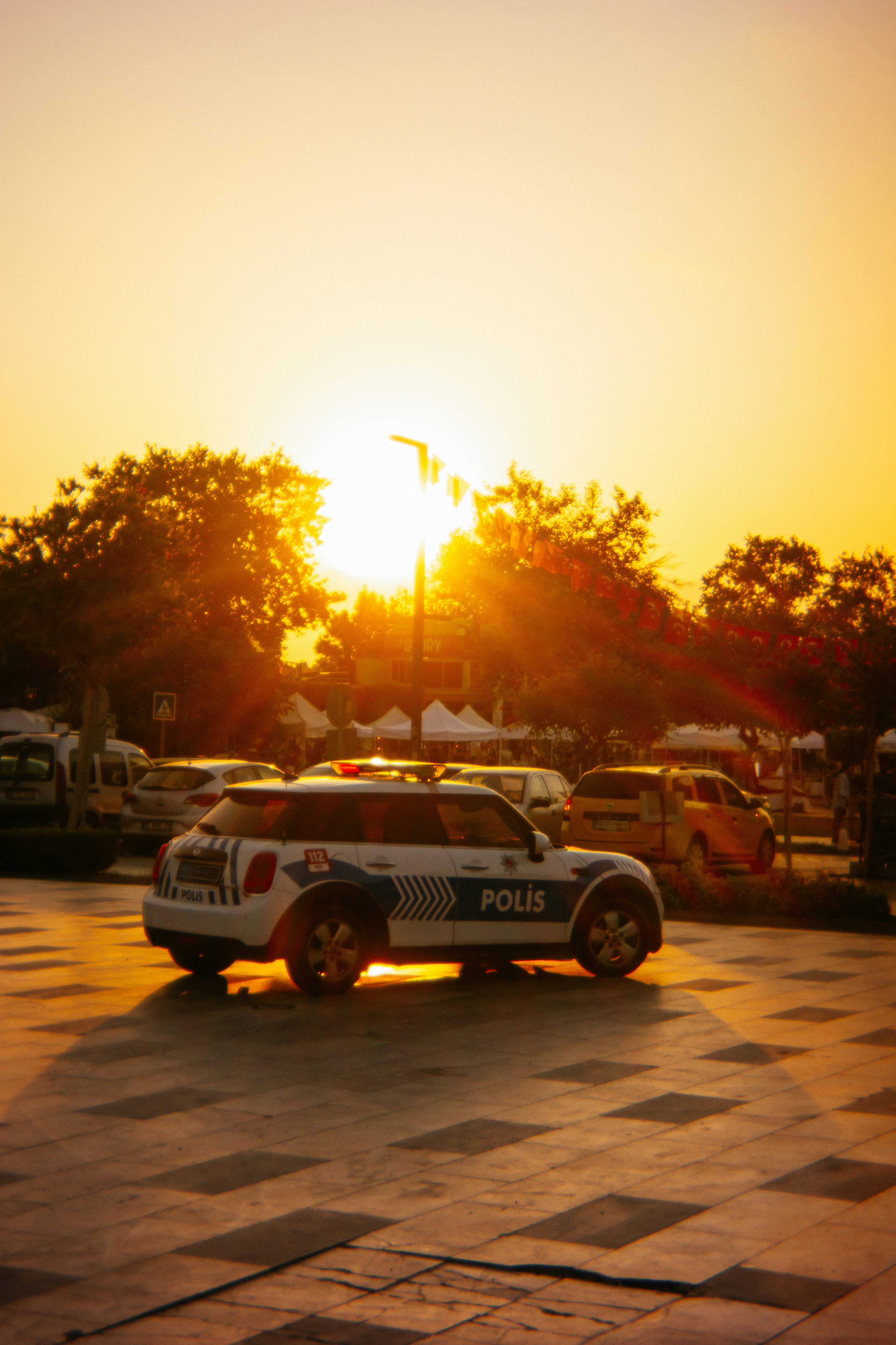 Backlit Square: Police SUV in a Sunlit Market Plaza at Dusk