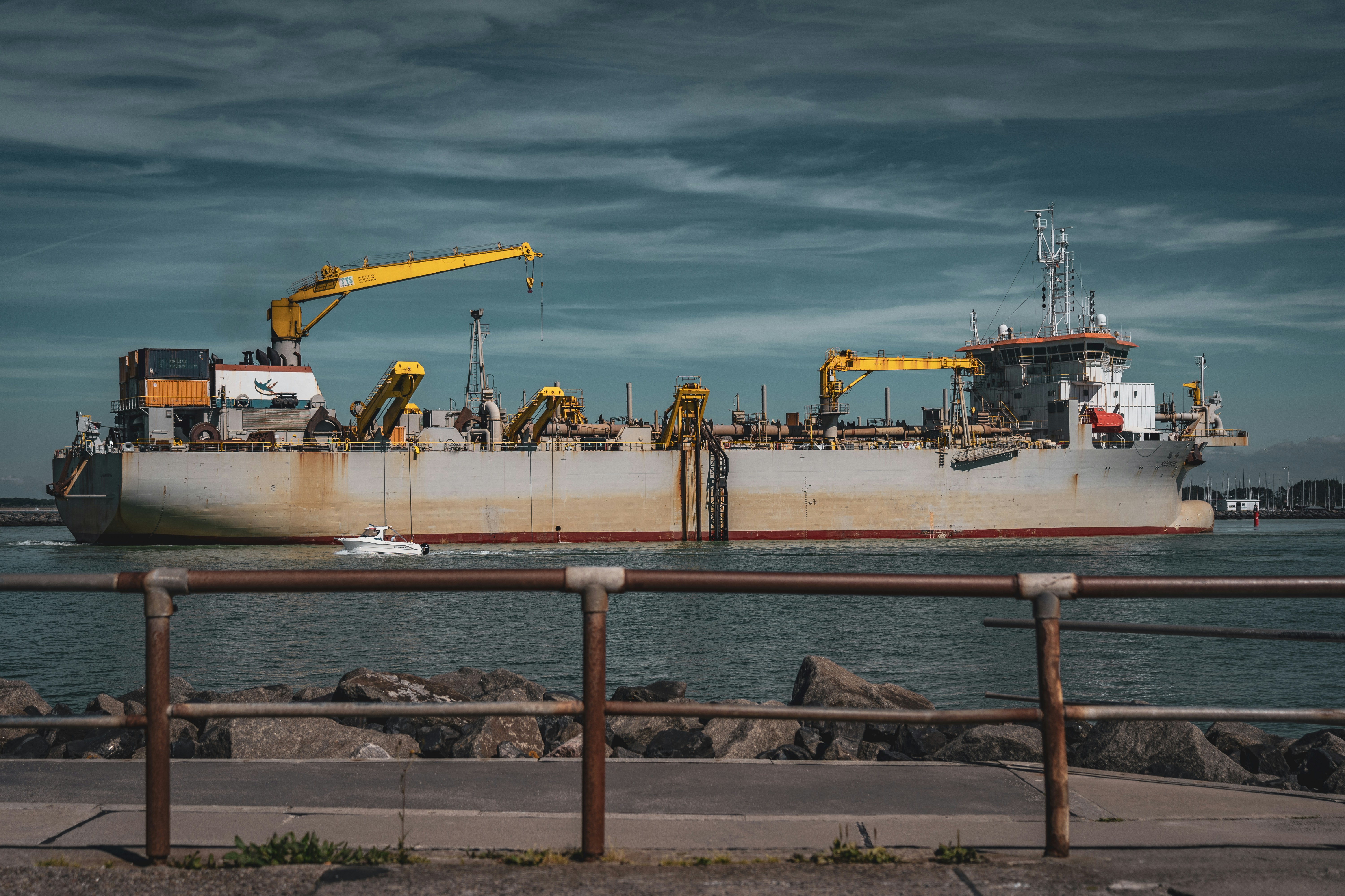 Large dredging vessel with yellow cranes docked under a cloudy sky.