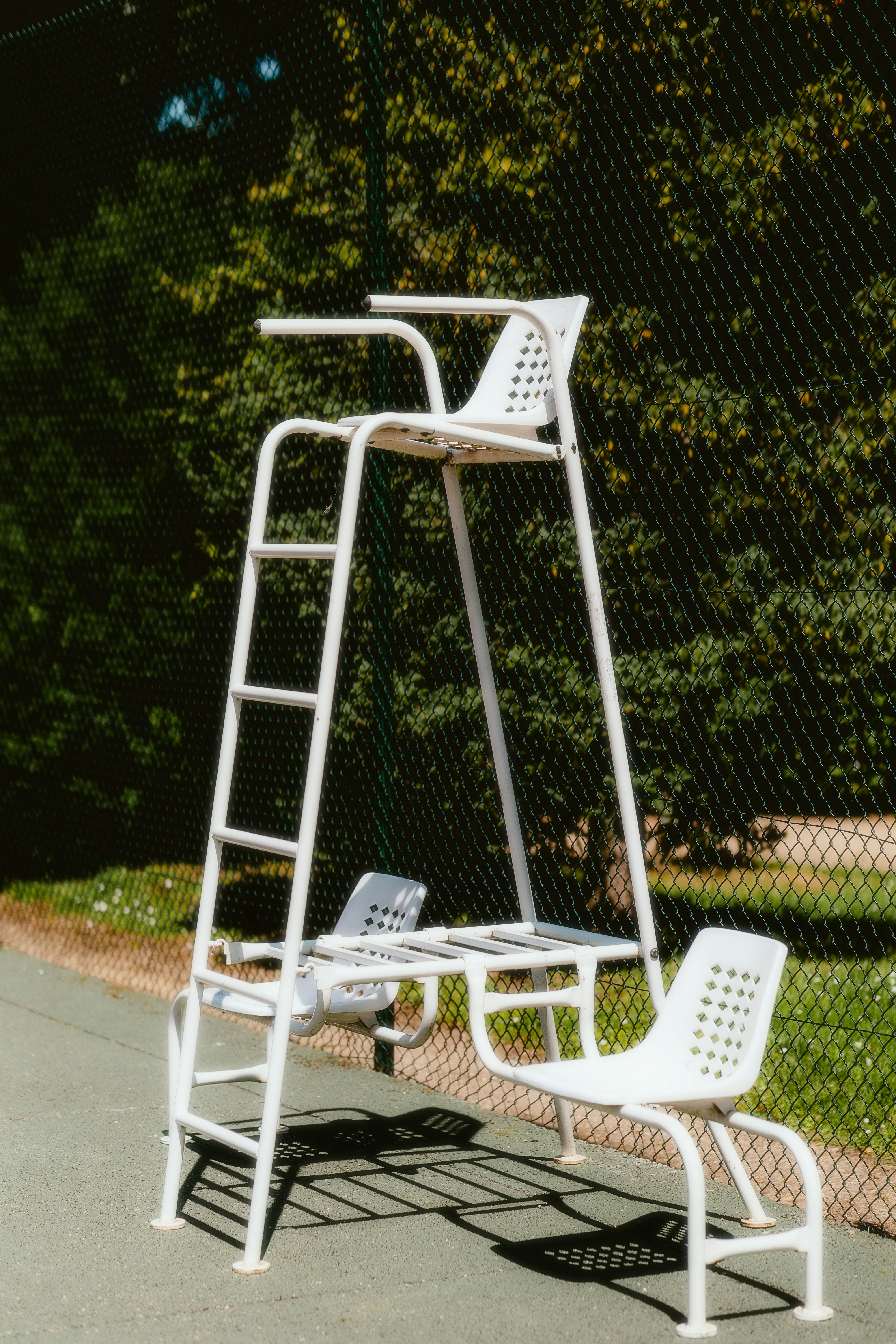 Elevated White Chair Silhouette against a Chain-Link Fence on a Sunlit Court