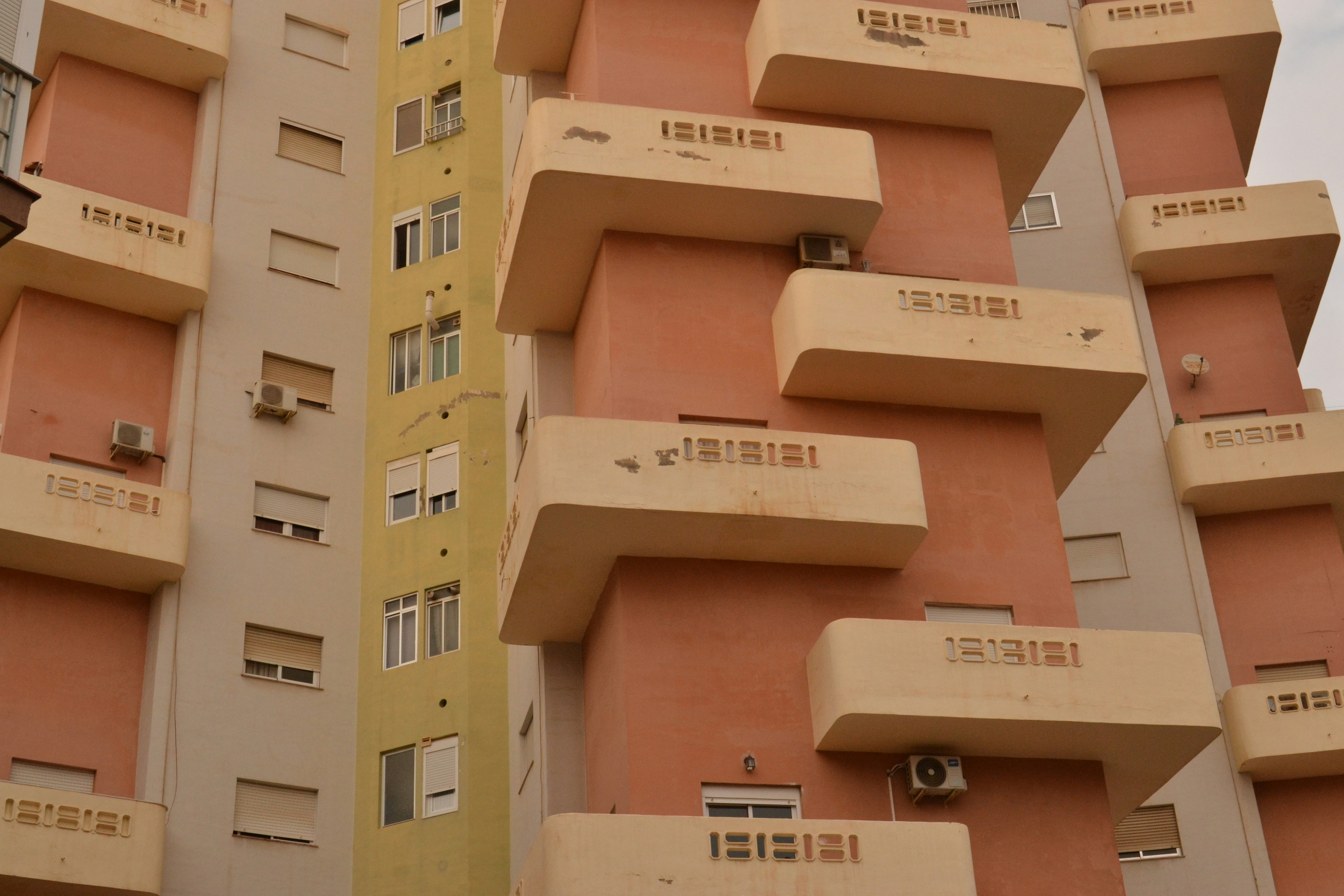 High-rise building with staggered balconies and numerous windows against a muted sky.