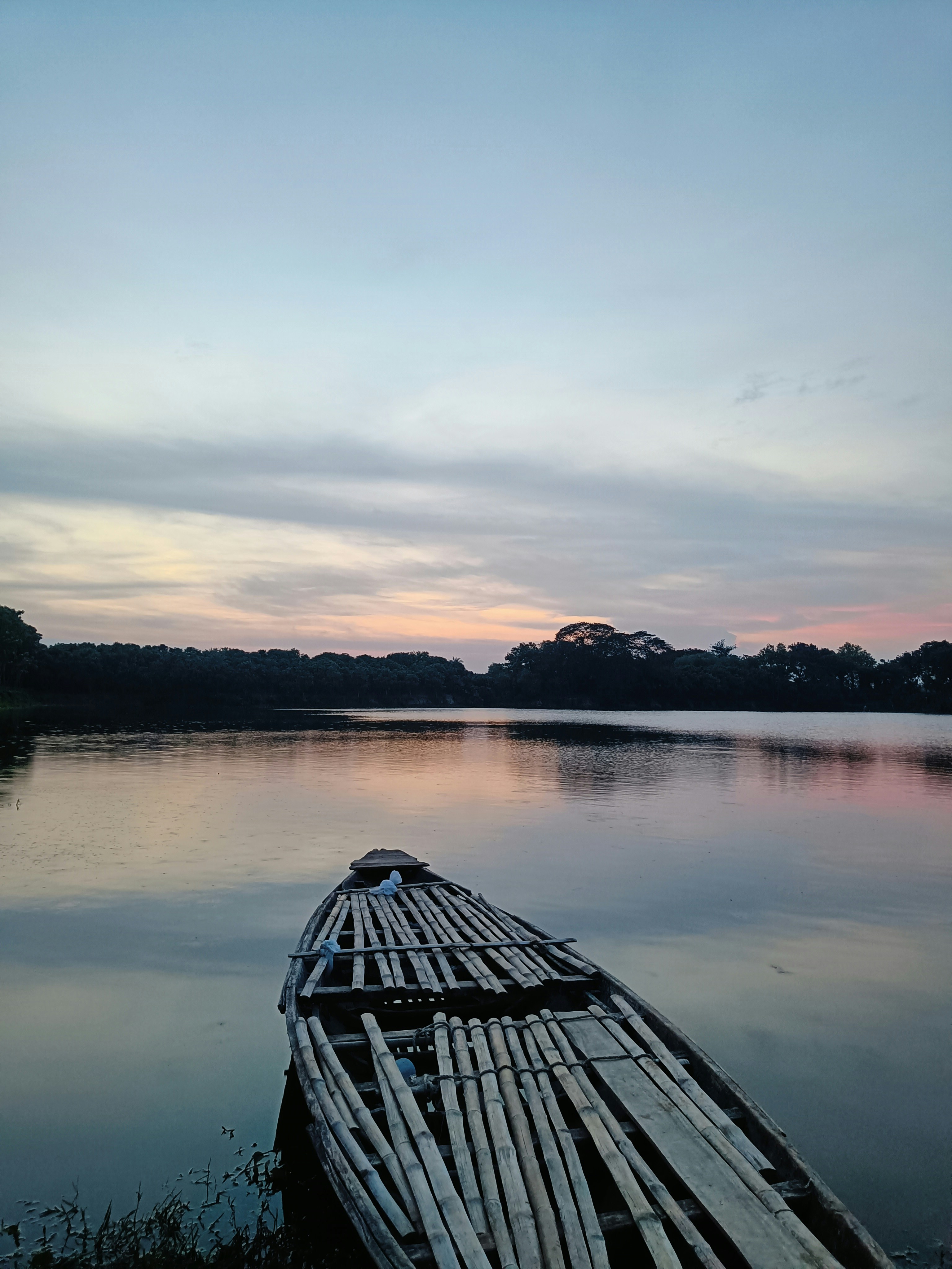 "A tranquil evening scene with a lone boat resting on the bank of a vast pond, bathed in the soft, golden hues of the setting sun."