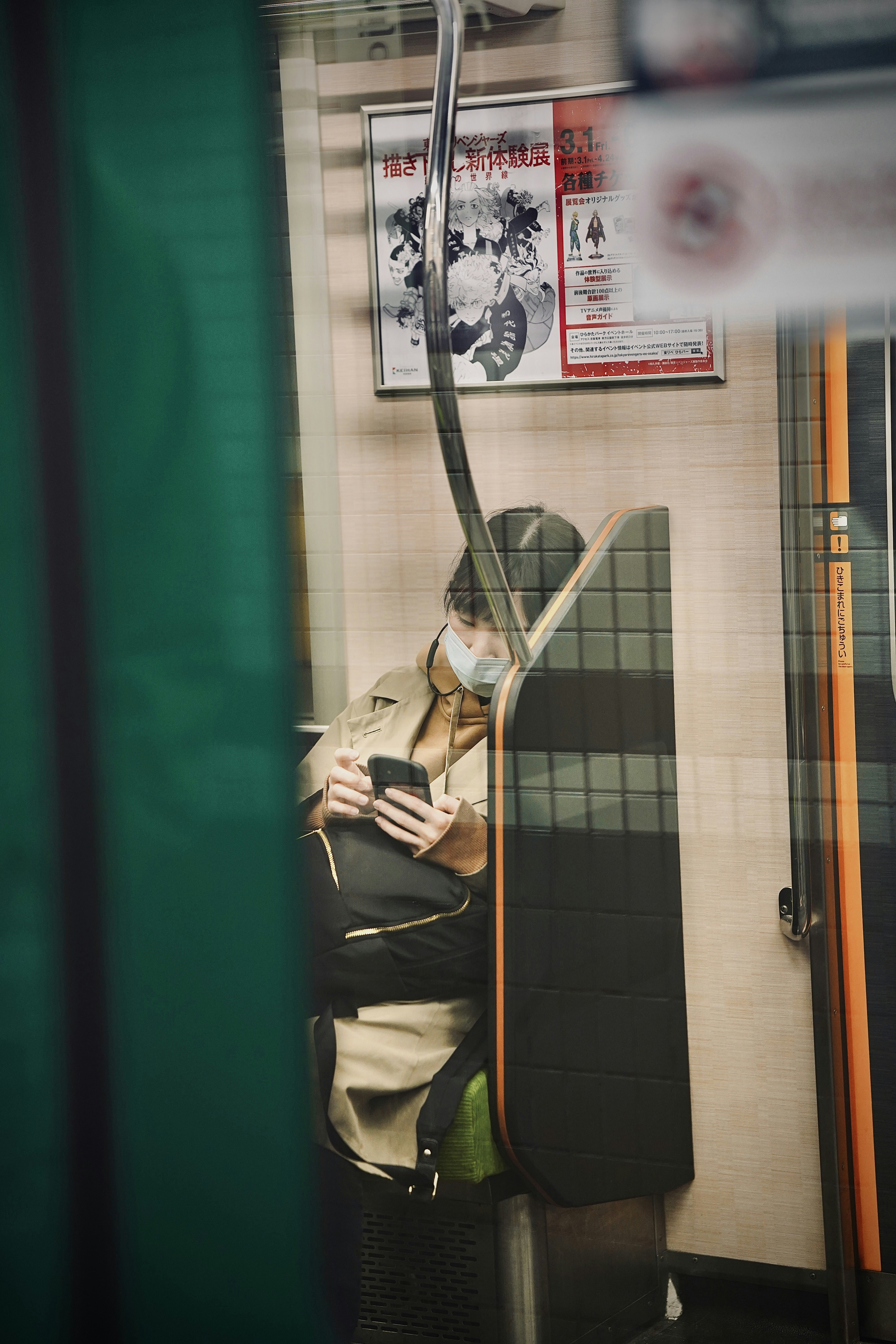 Transit Portrait: A masked commuter engrossed in a phone beneath subway posters