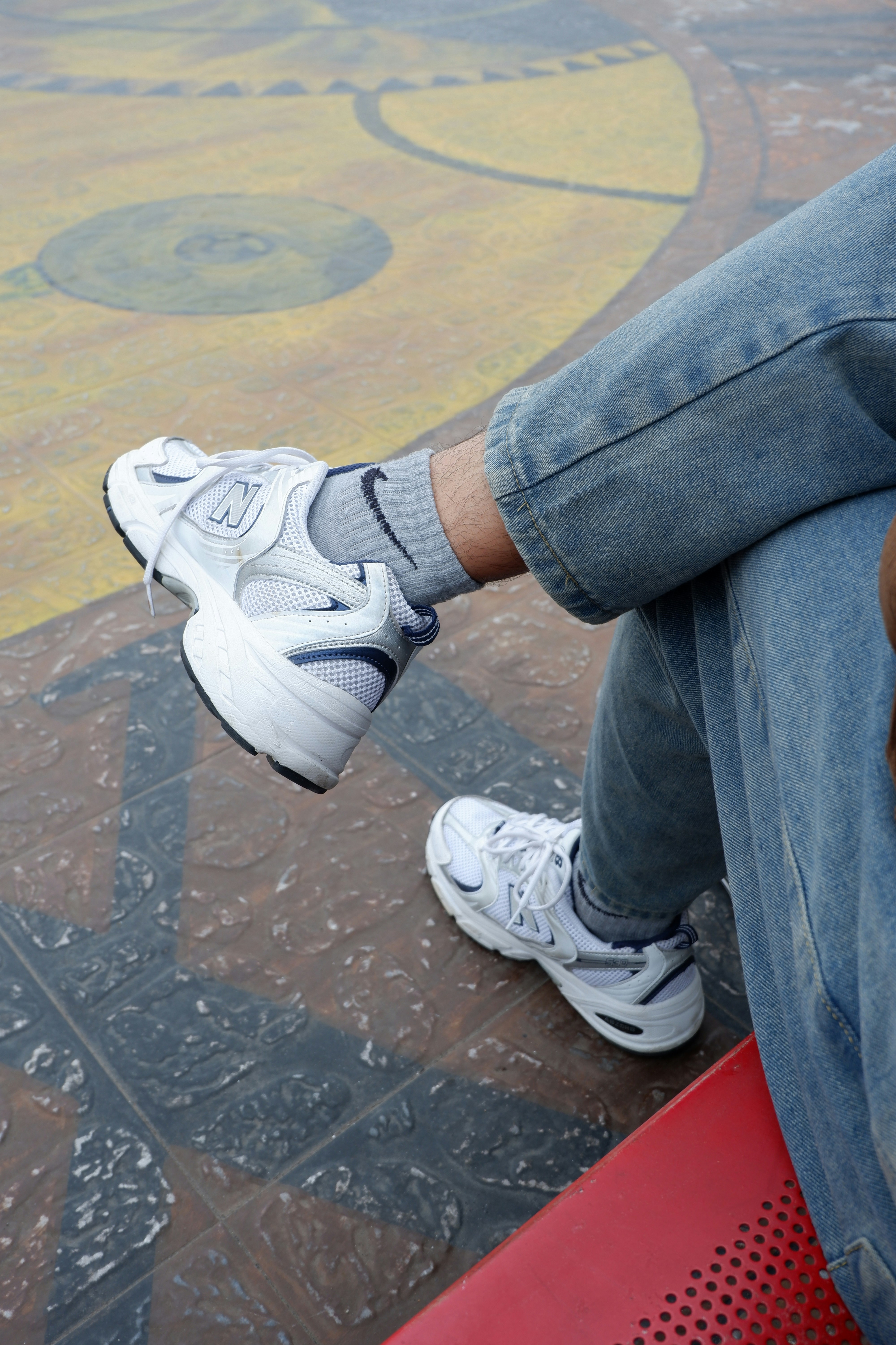 Paused on Painted Pavement: White New Balance Sneakers by a Rain-Slick Mosaic