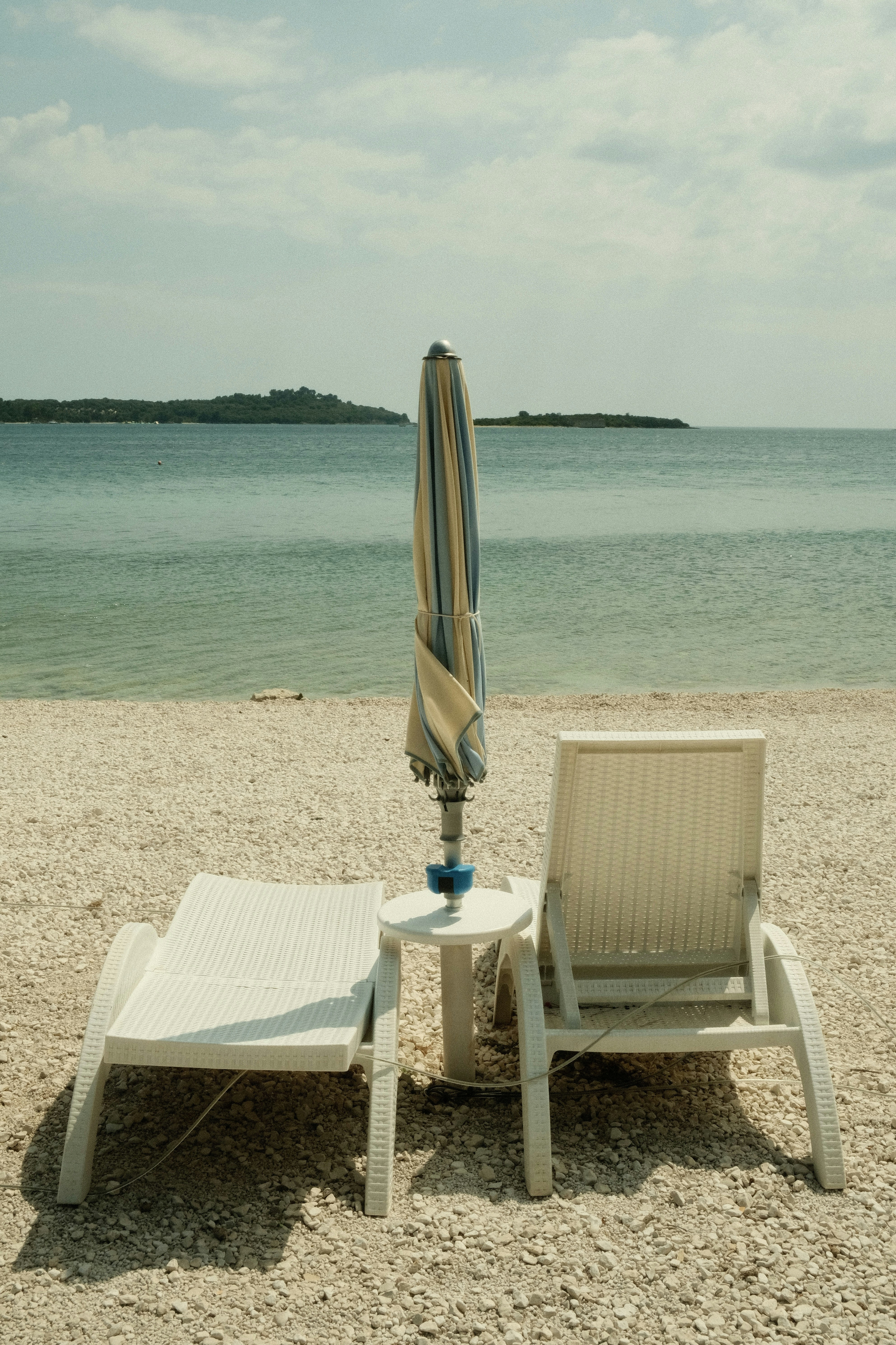 Umbrella Sentinel: Quiet Morning Between Chairs on a Pebble Beach