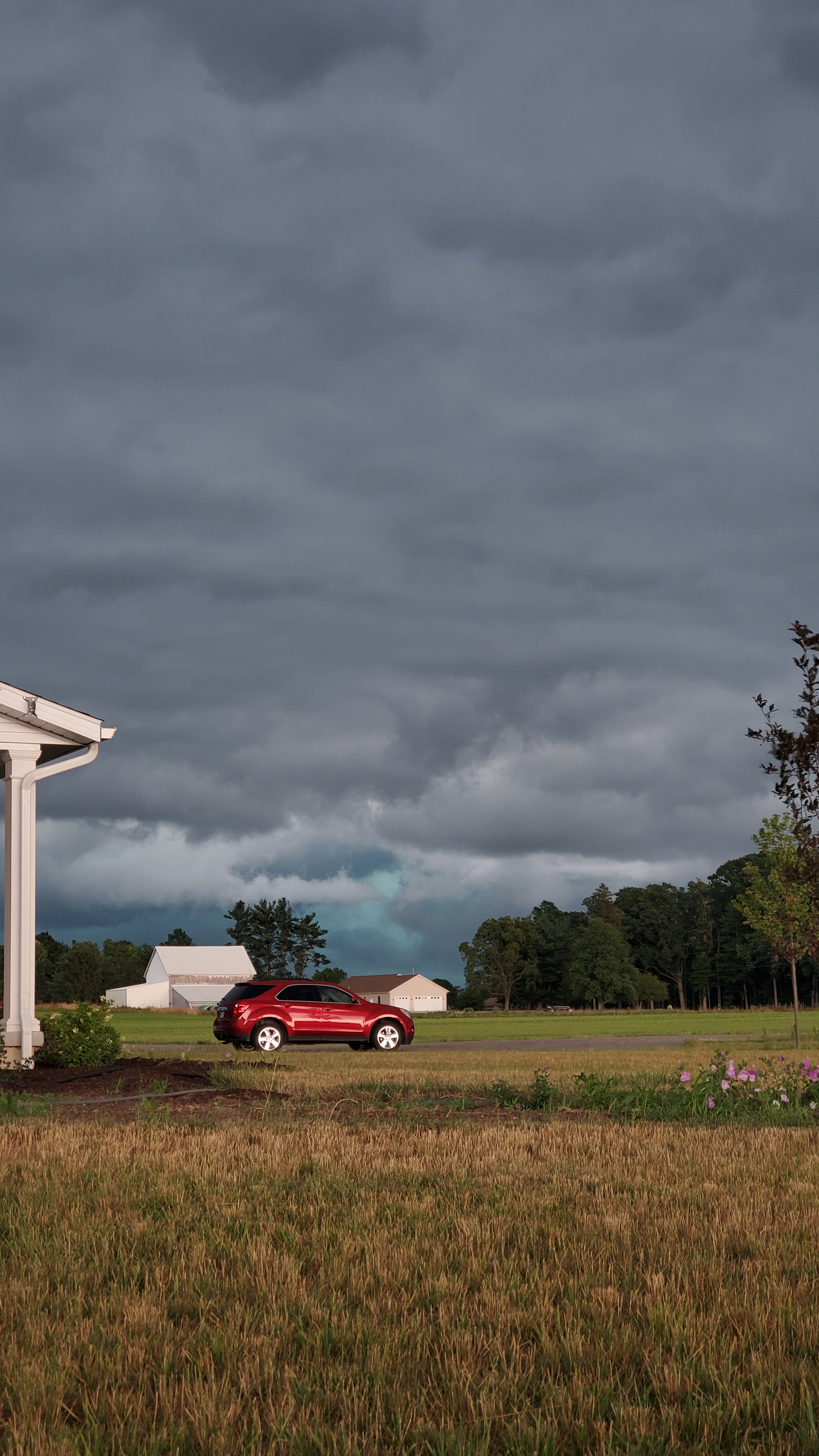 Red SUV at the Farmstead: Quiet Yard Beneath a Looming Sky